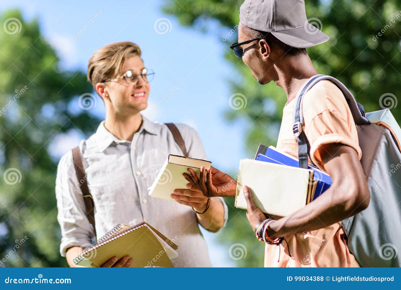 Handsome Multiethnic Students Holding Books And Looking At Each Other ...