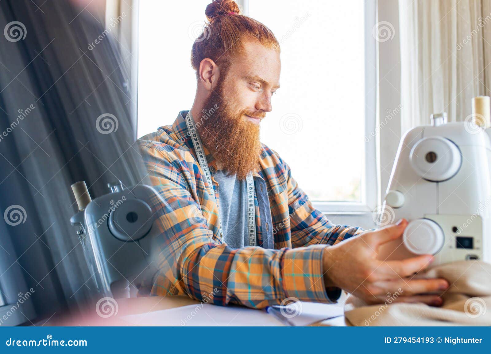 Handsome Redhaired Man with Long Beard Sews at a Sewing Machine at Home ...