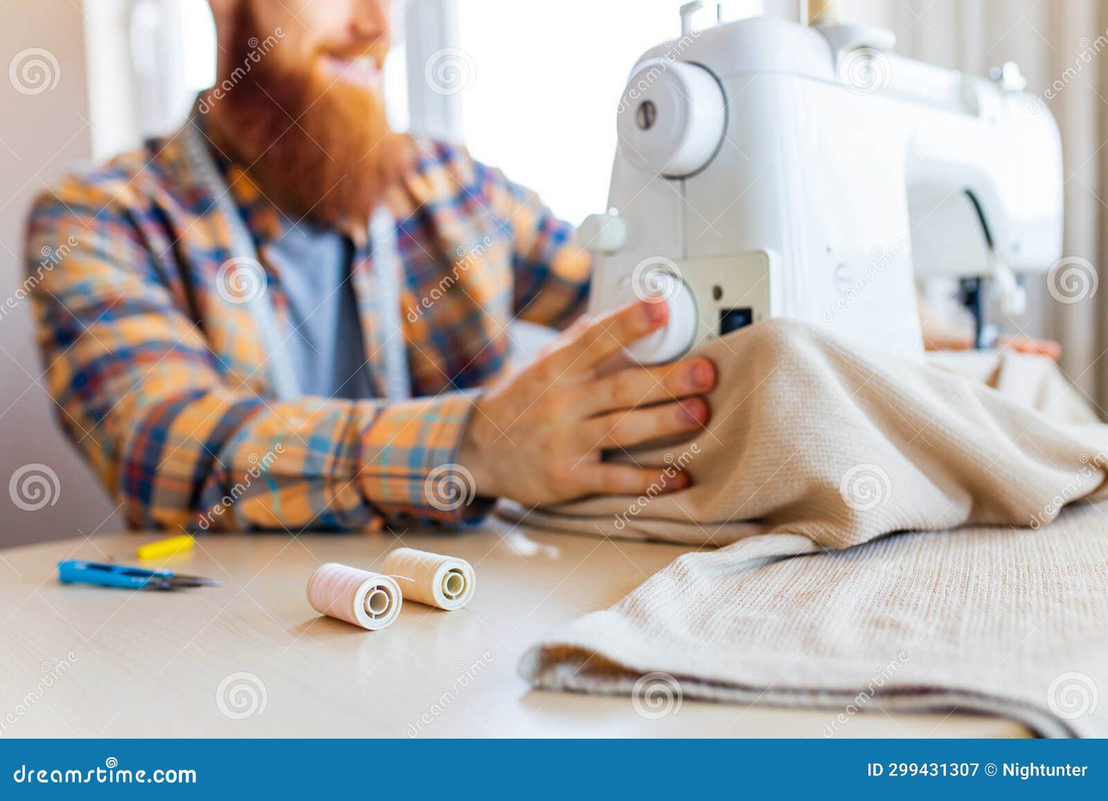 Handsome Redhaired Man with Long Beard Sews at a Sewing Machine at Home ...