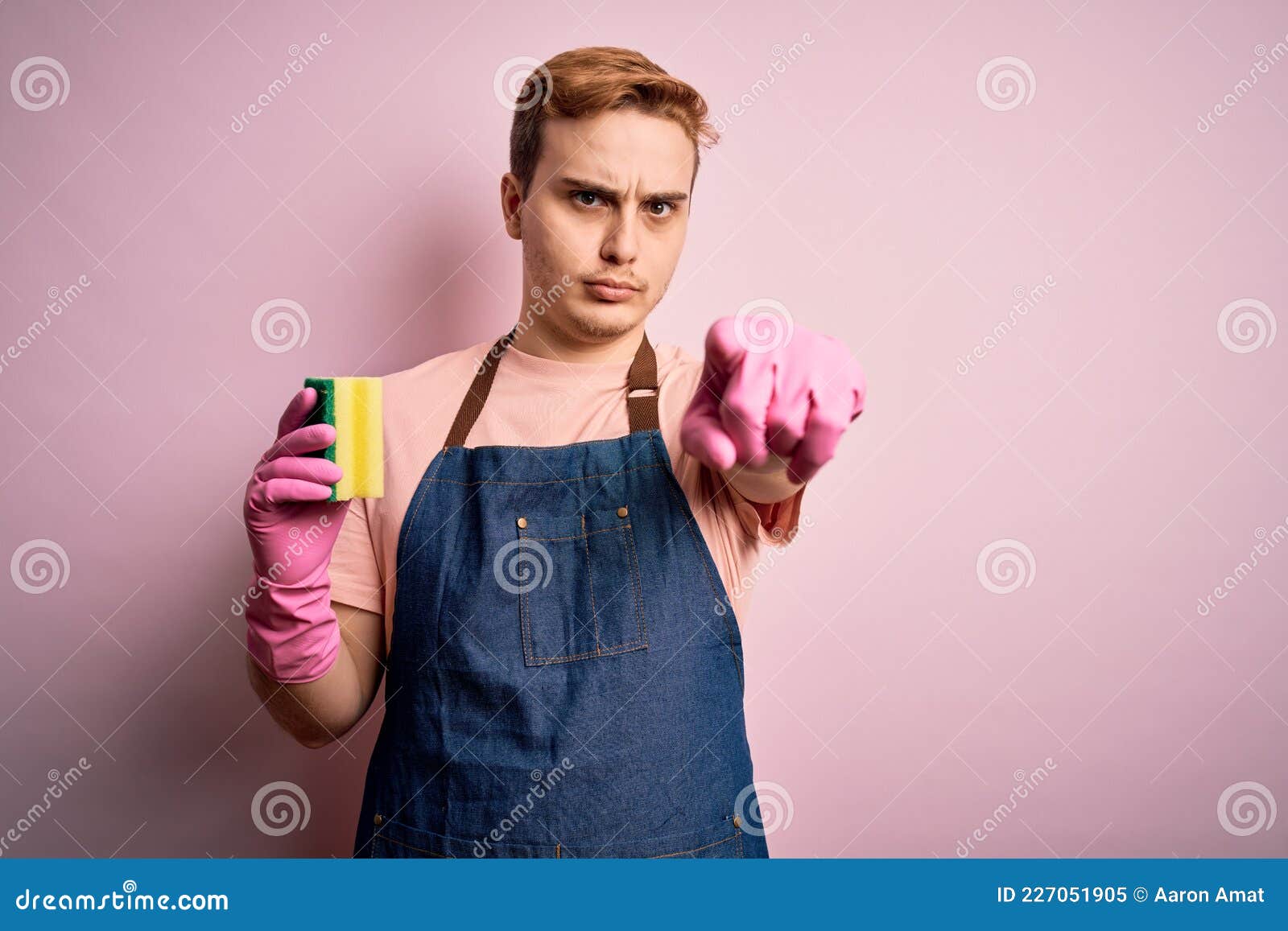Handsome Redhead Man Doing Housework Wearing Apron And Gloves Using Cleaner Scourer Pointing