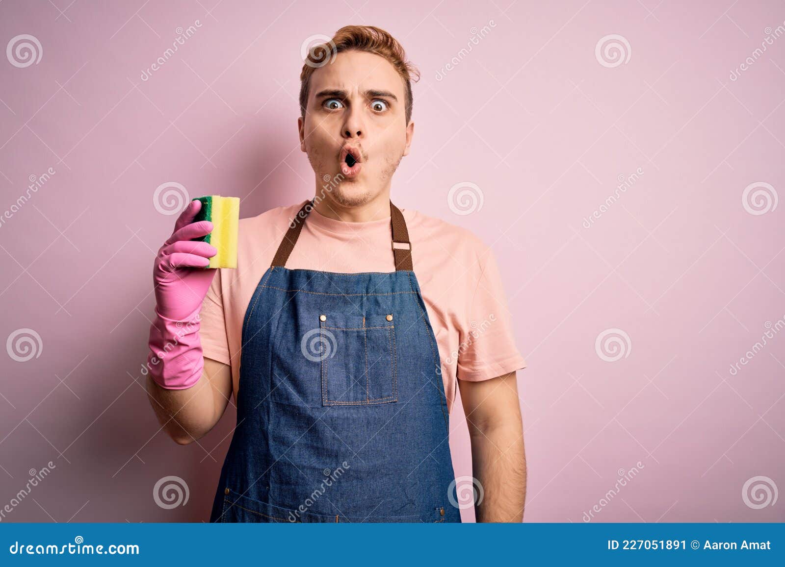 Handsome Redhead Man Doing Housework Wearing Apron And Gloves Using Cleaner Scourer Scared And