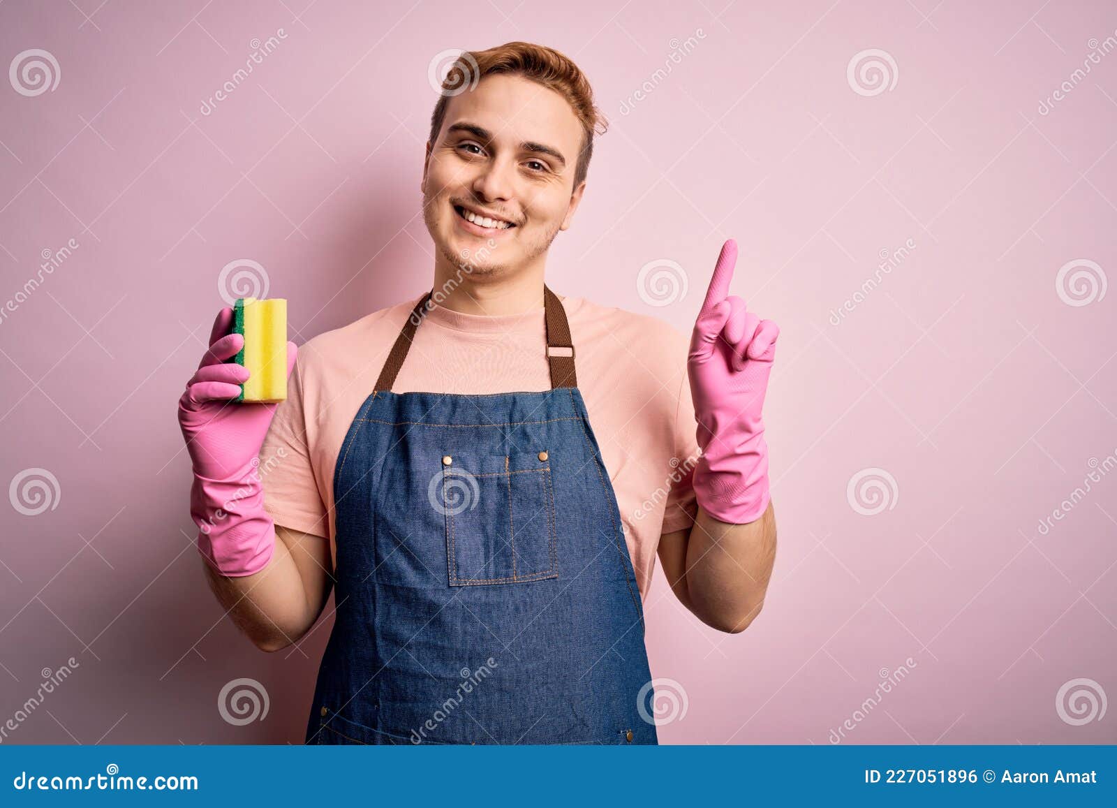 Handsome Redhead Man Doing Housework Wearing Apron And Gloves Using Cleaner Scourer Surprised