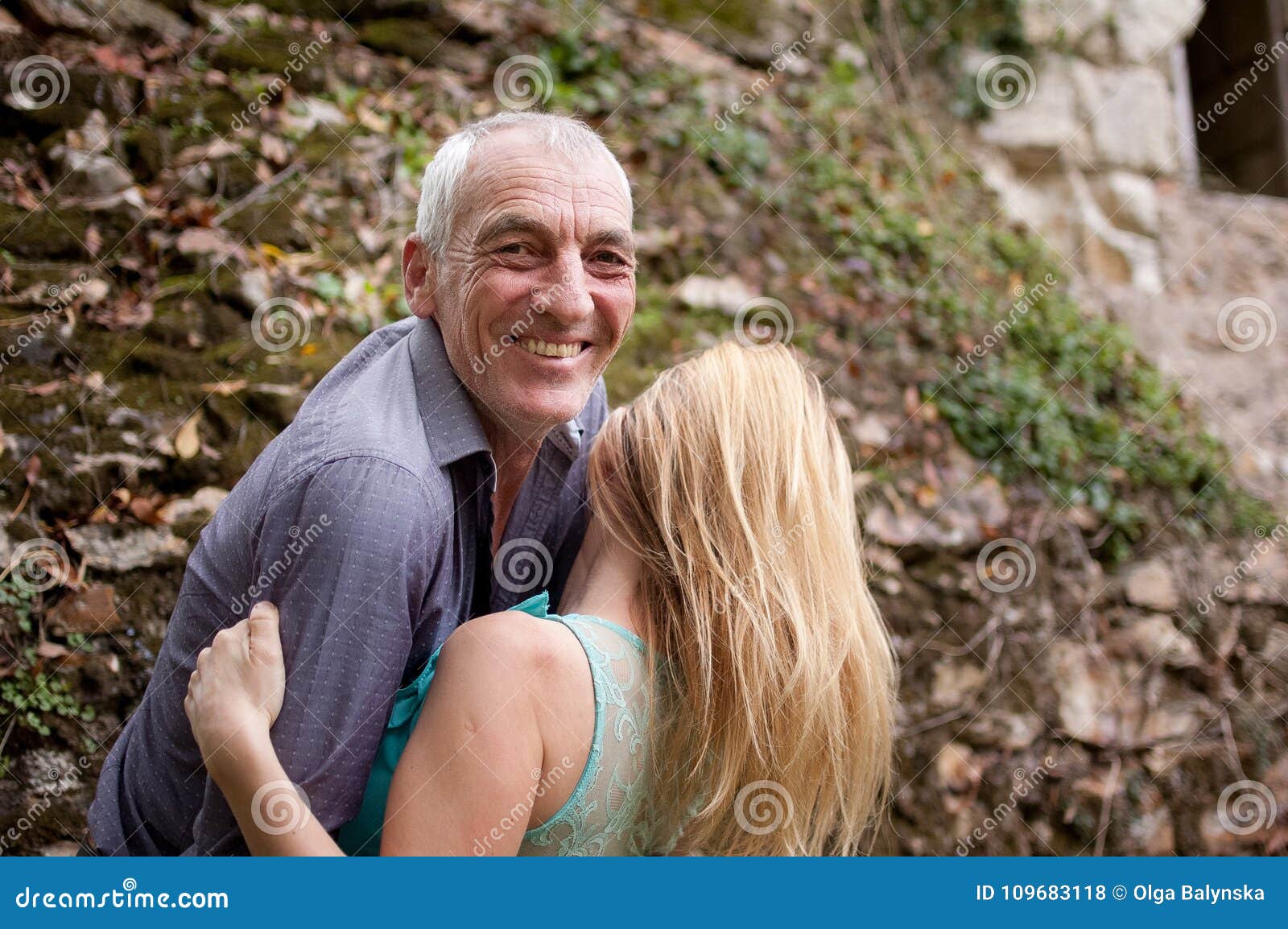 Handsome Senior Man Hugging His Young Girlfriend Outdoors And Smiling