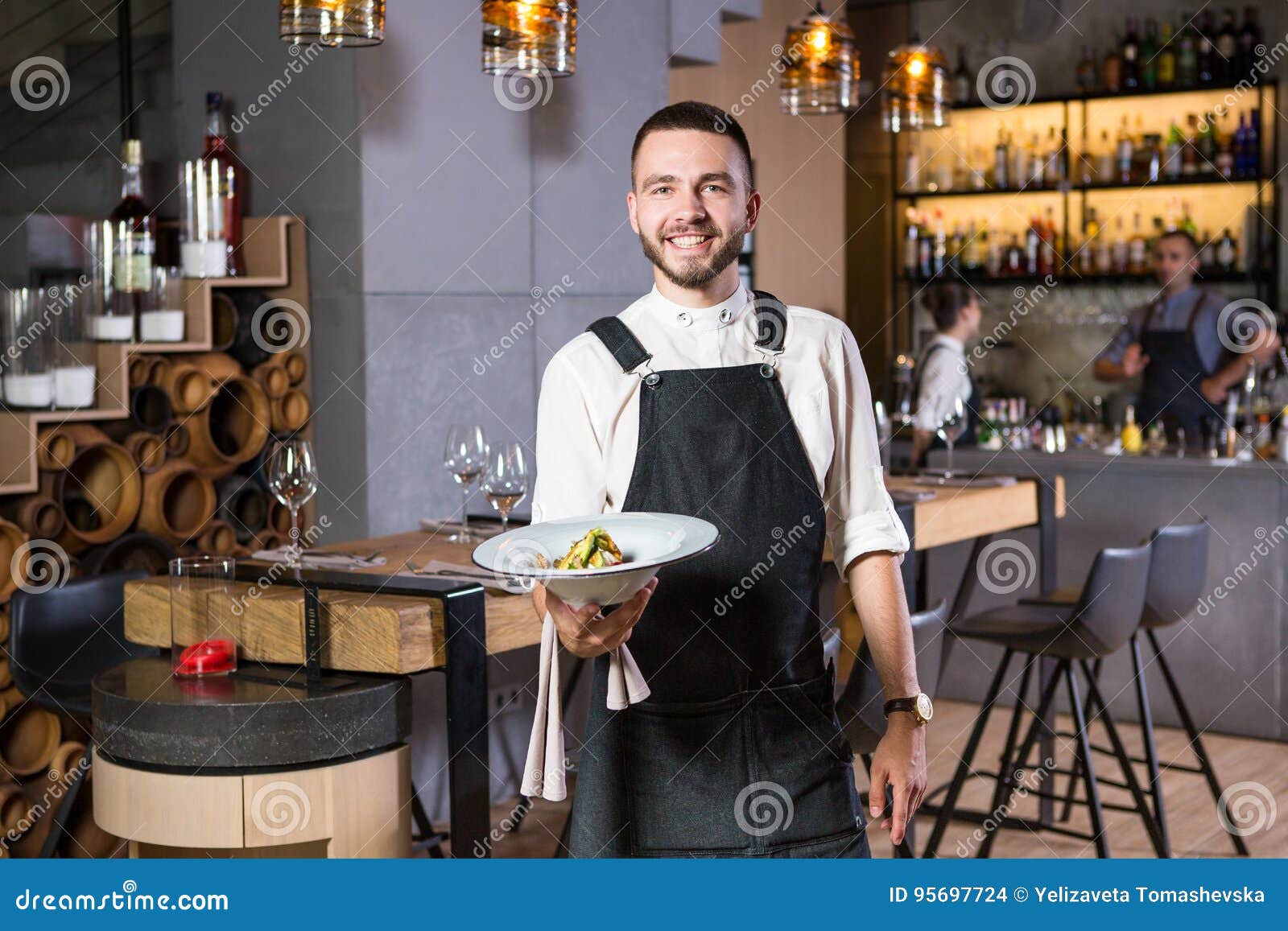 A Handsome Young Guy with a Beard Dressed in an Apron Standing in a ...