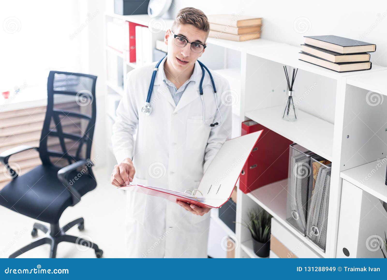 A Young Doctor in a White Robe Standing Near the Rack and Holding a ...