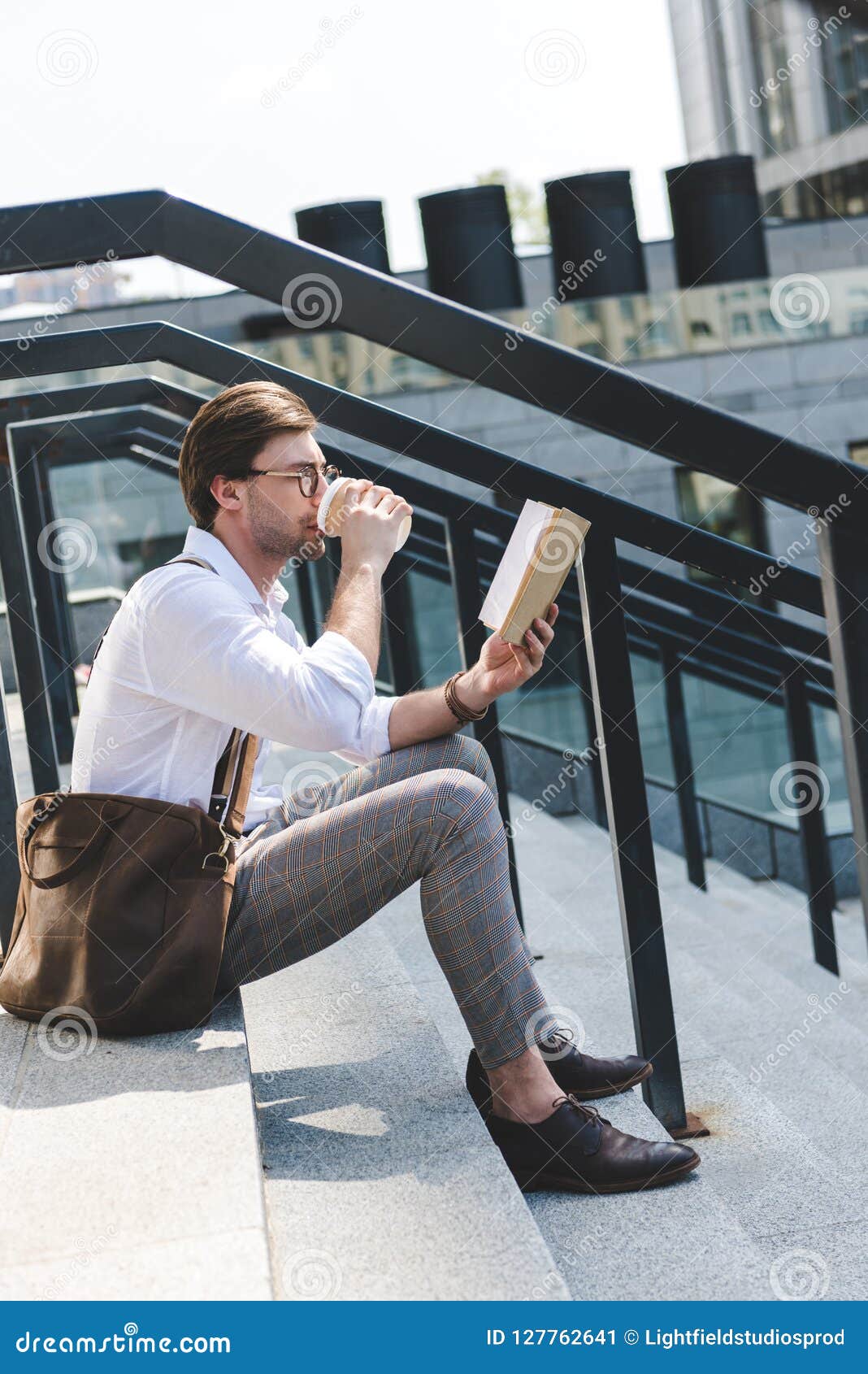 Handsome Young Man Drinking Coffee from Paper Cup and Reading Book on ... Handsome Young Man Drinking Coffee from Paper Cup and Reading Book on ...