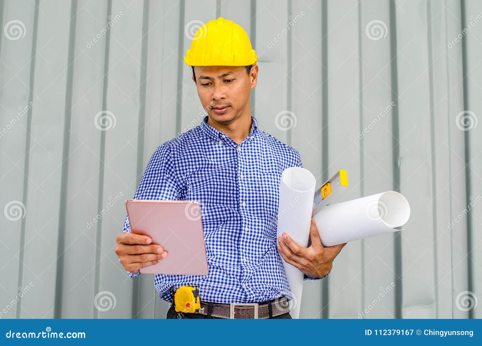 Handsome Young Man in Hardhat Holding Blueprint and Using Tablet while ...