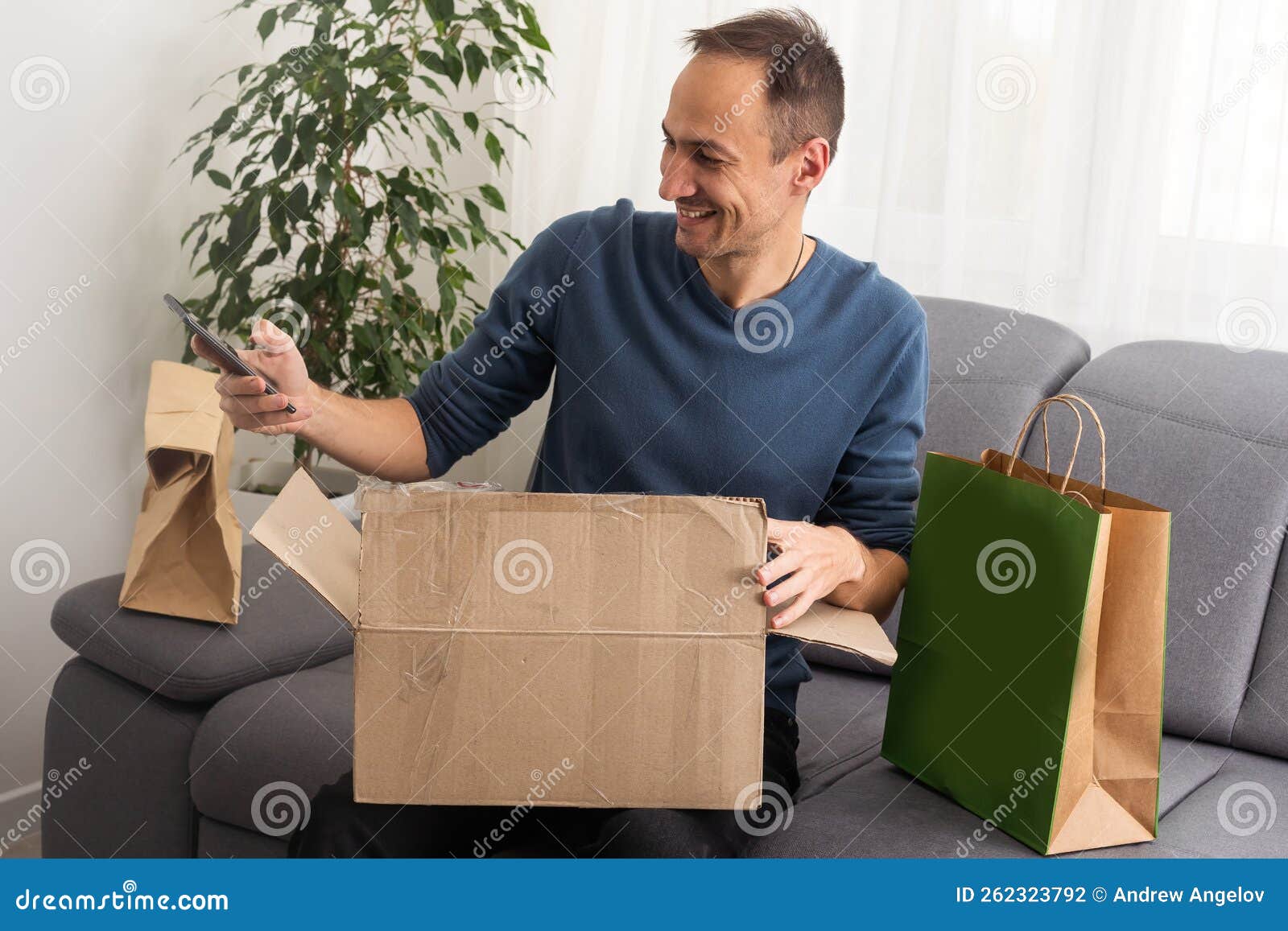 Handsome Young Man Opening Box with Parcel while Sitting on Sofa at ...