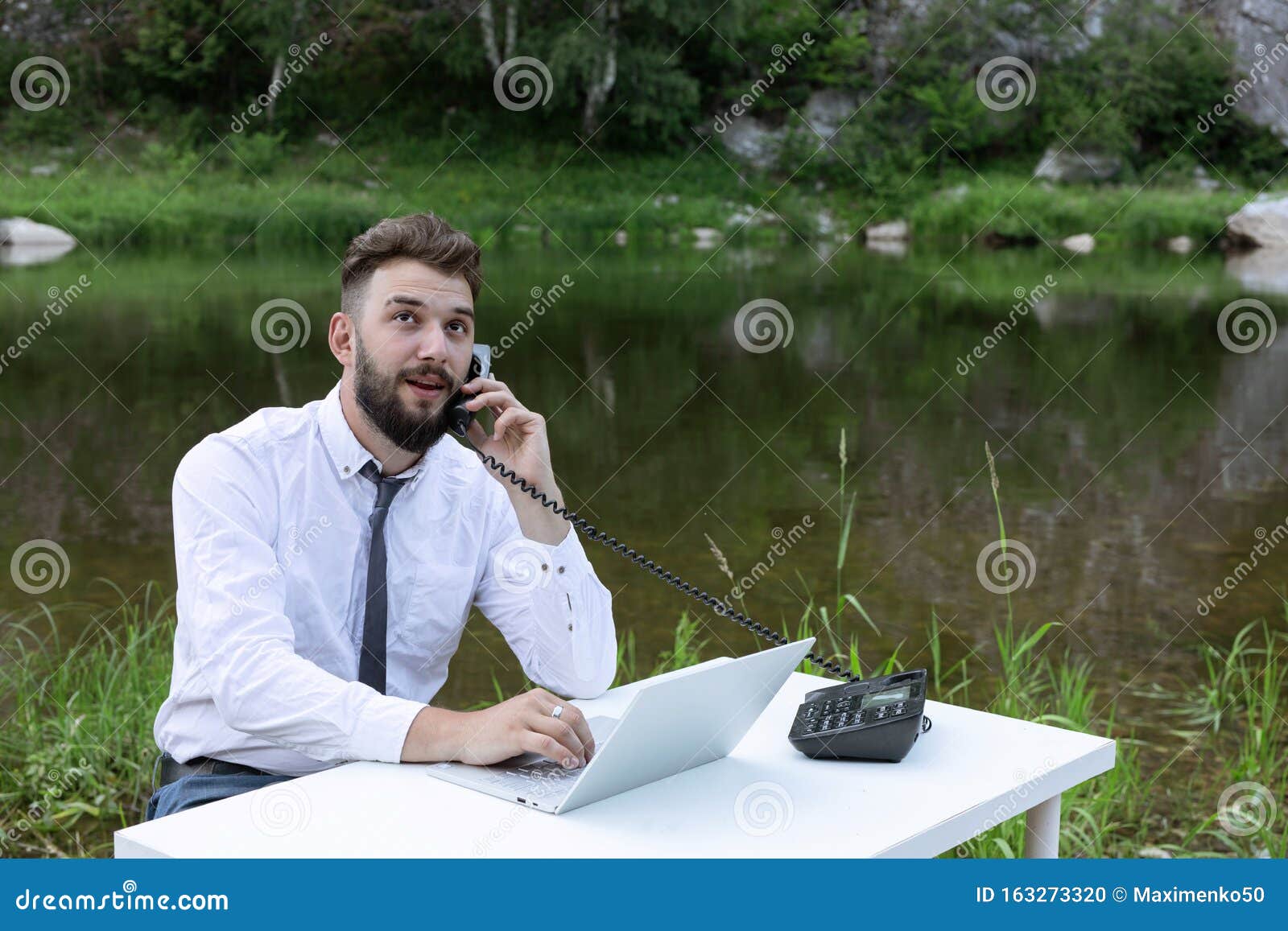 Handsome Young Man Talking on Phone and Using the Computer while ...