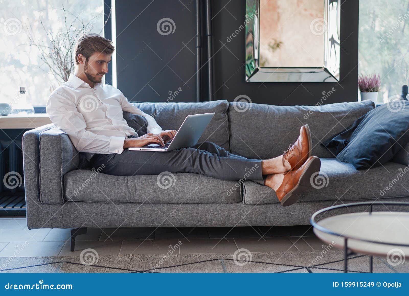 Multitasking. Handsome Young Man Working with Laptop while Sitting on ... Multitasking. Handsome Young Man Working with Laptop while Sitting on ...