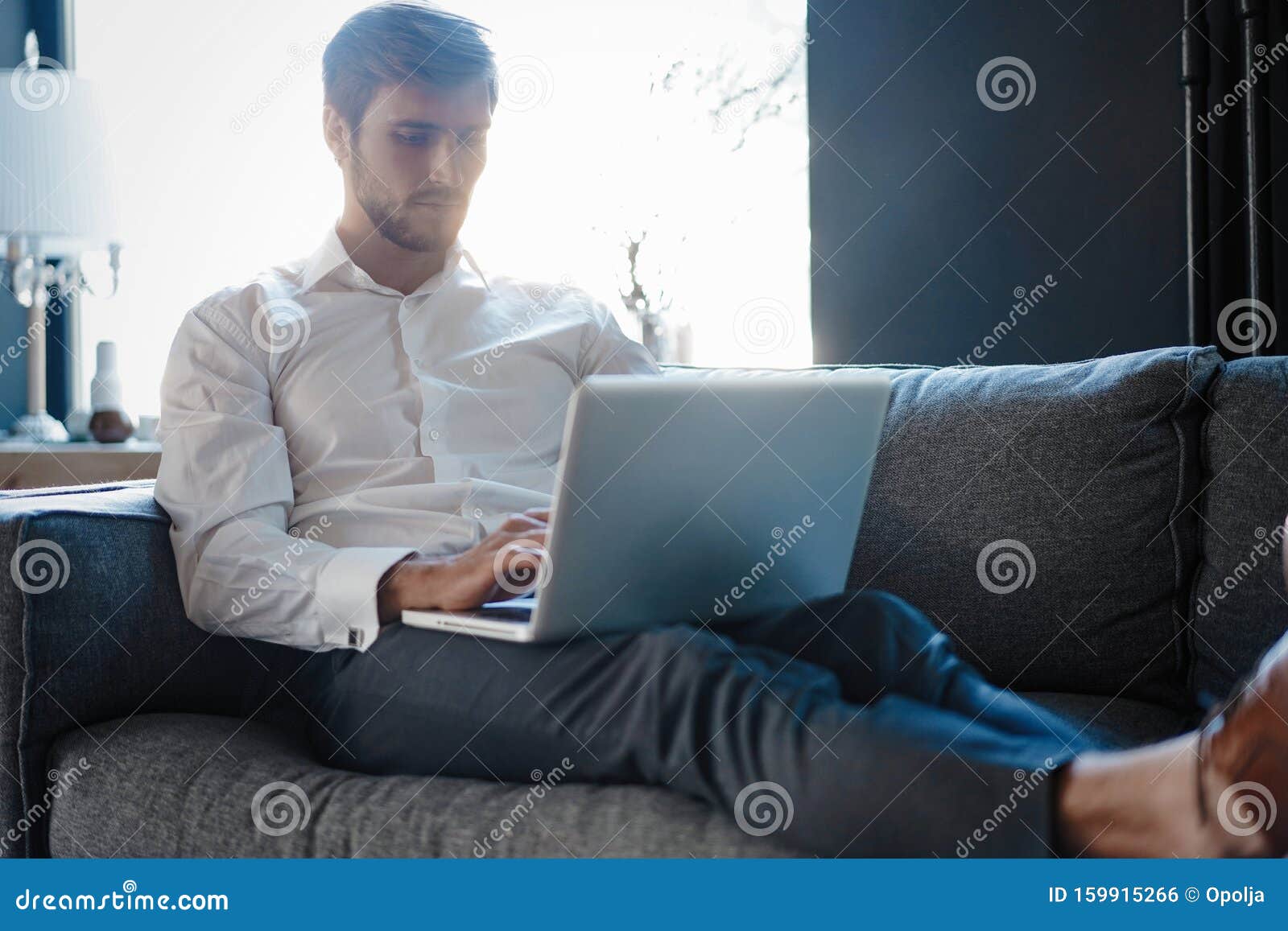Multitasking. Handsome Young Man Working with Laptop while Sitting on ... Multitasking. Handsome Young Man Working with Laptop while Sitting on ...