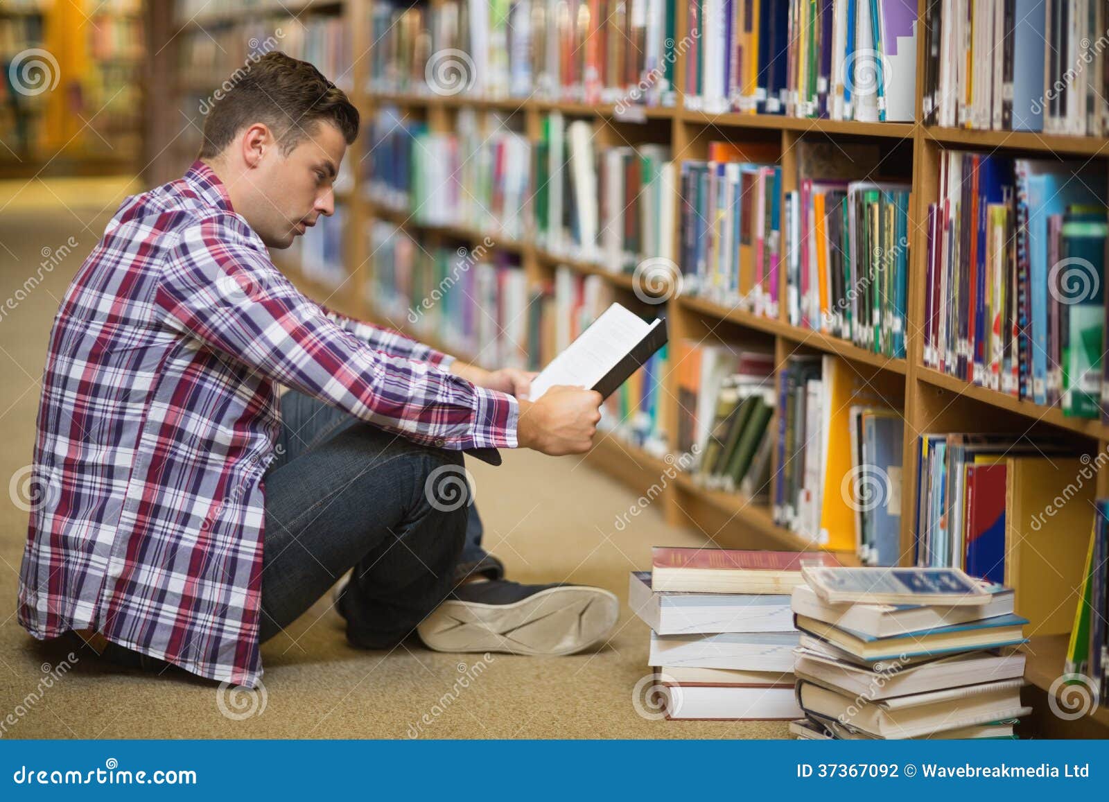 Handsome Young Student Sitting on Library Floor Reading Book Stock ...