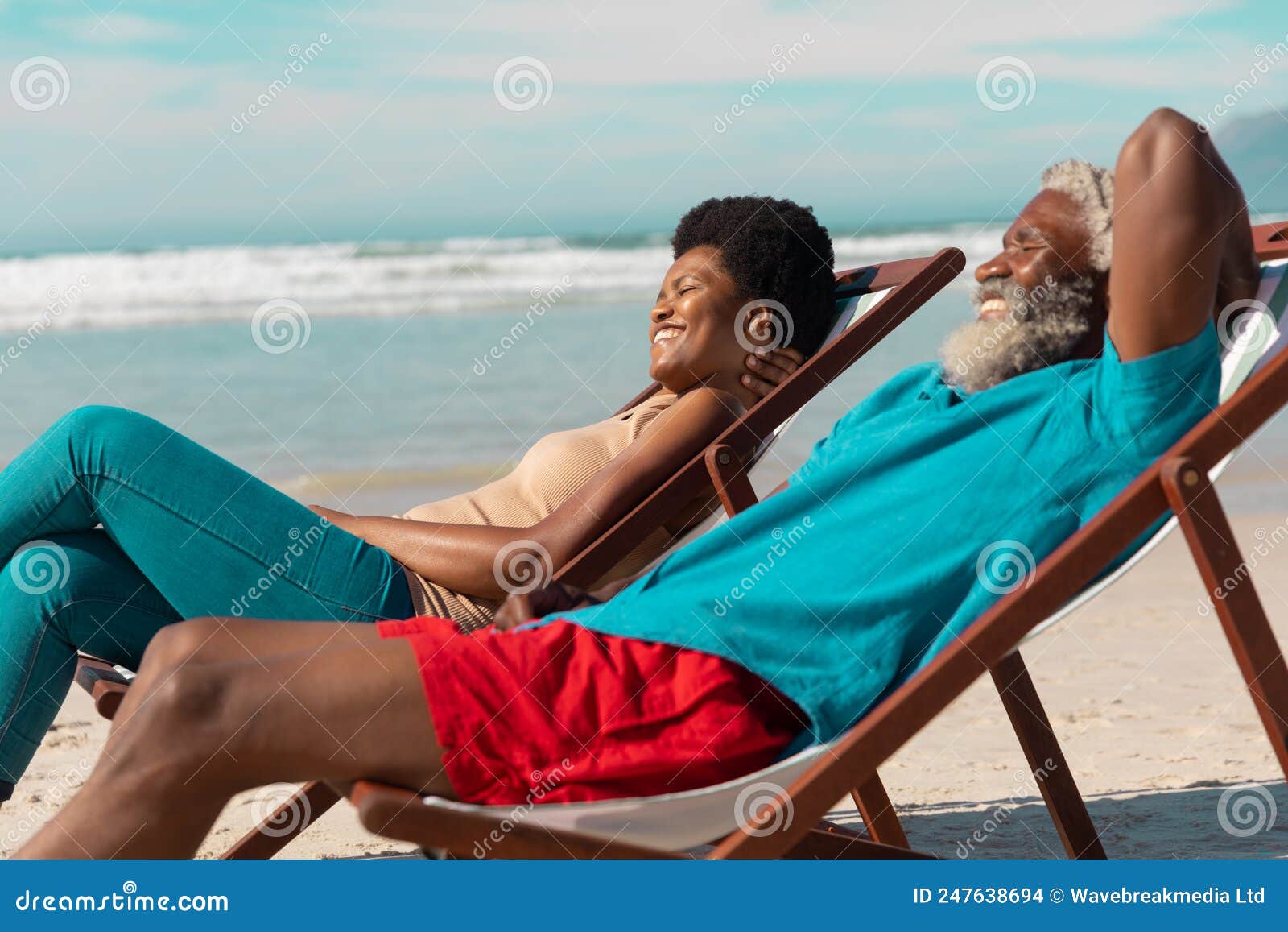 Happy African American Couple Relaxing On Deckchairs Against Sea And