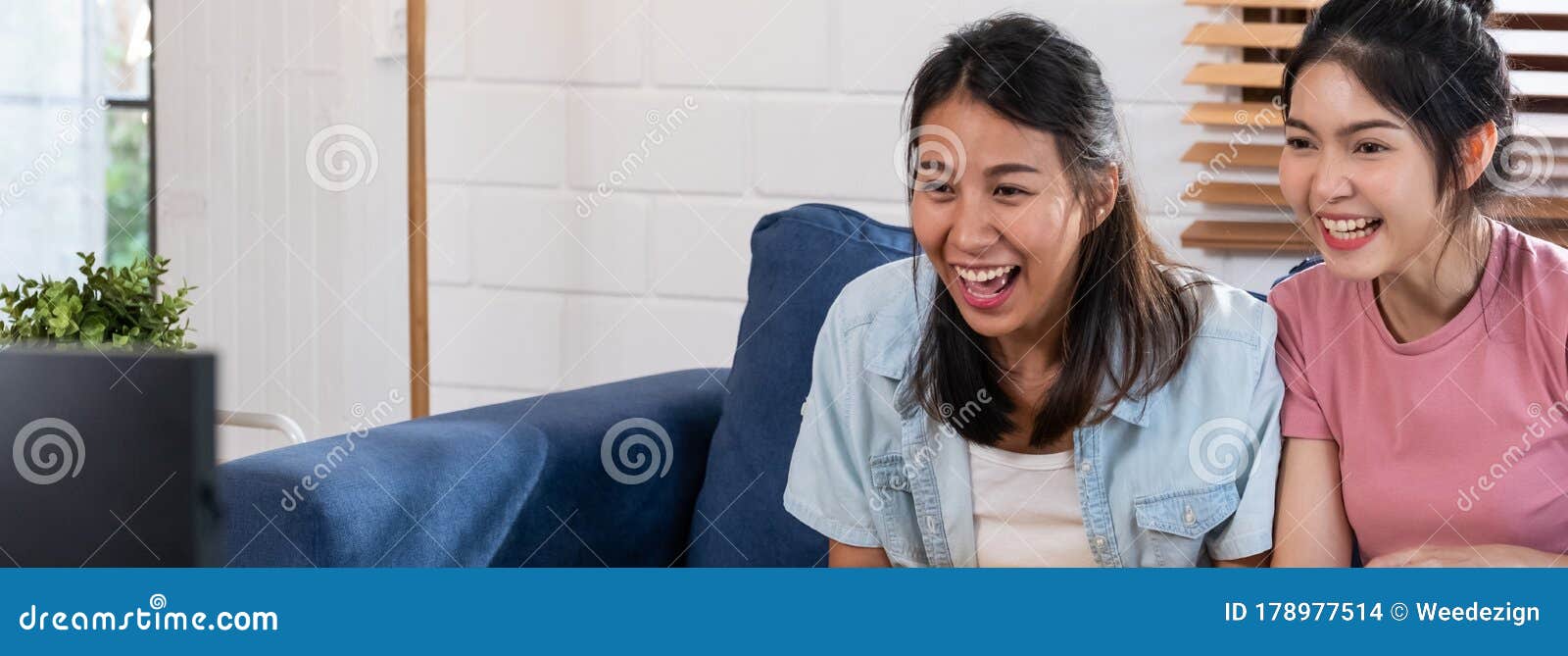 Happy Asian Lesbian Couple Watching Television Together At Sofa In