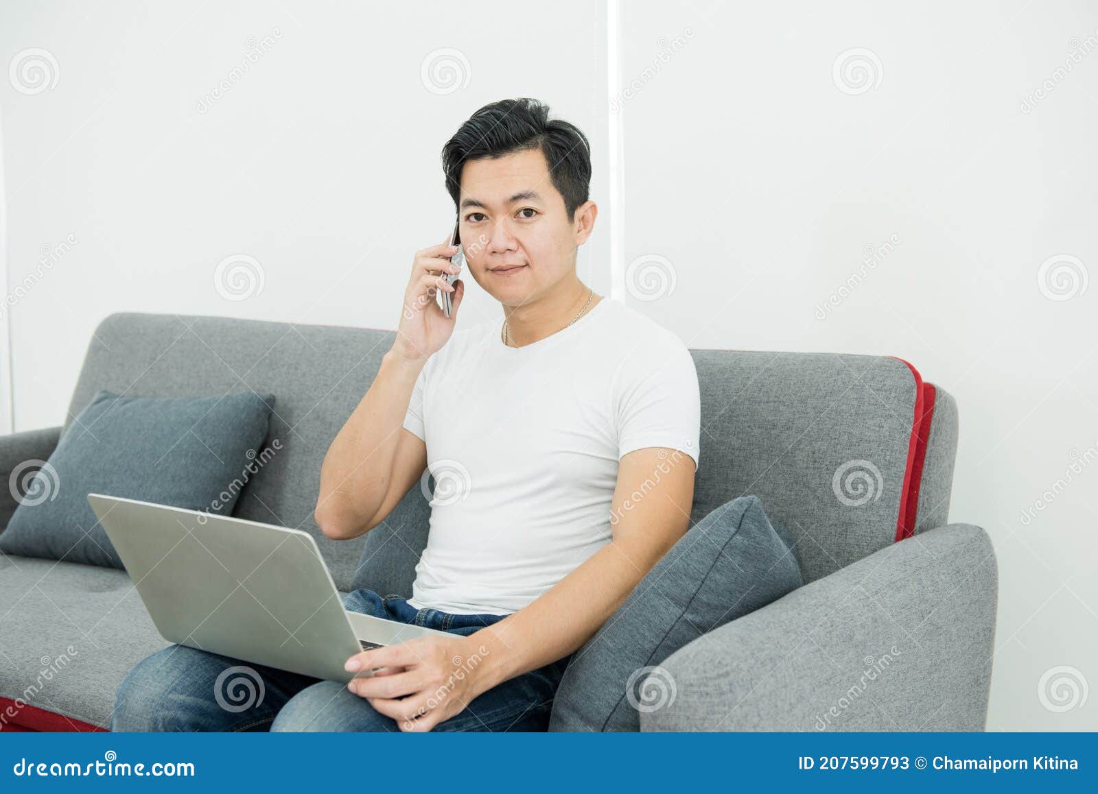 Happy Asian Man Talking on Smartphone while Sitting on Sofa and Using ...