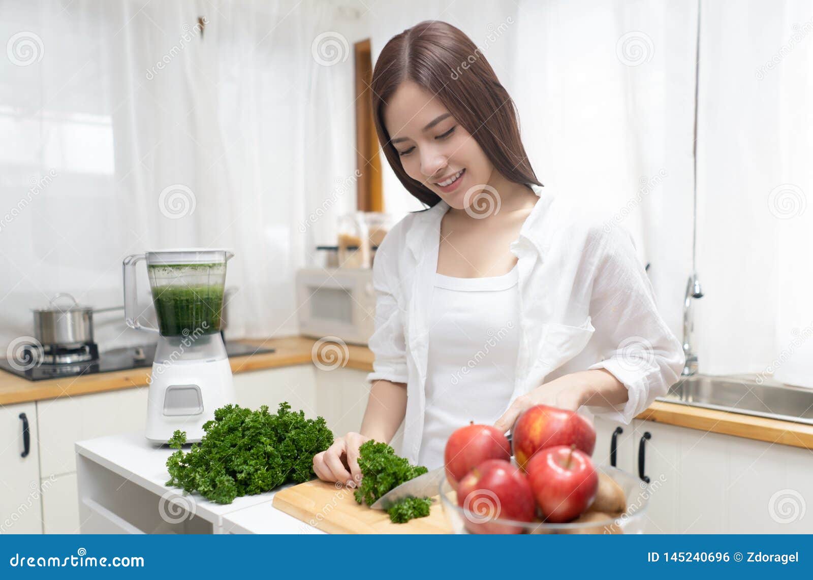 Happy Asian Woman Preparing Healthy Green Vegetables In Blender In Her