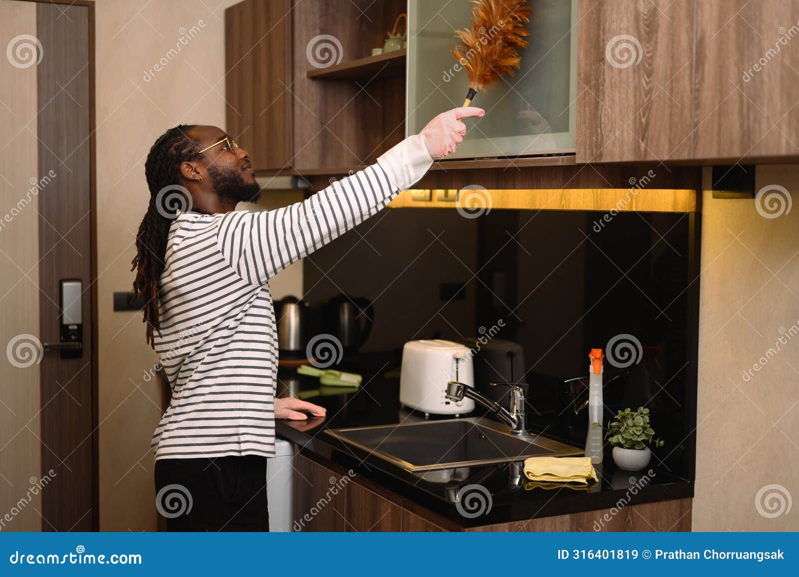 Happy Bearded African Man Dusting Shelf with a Feather Duster at Modern ...