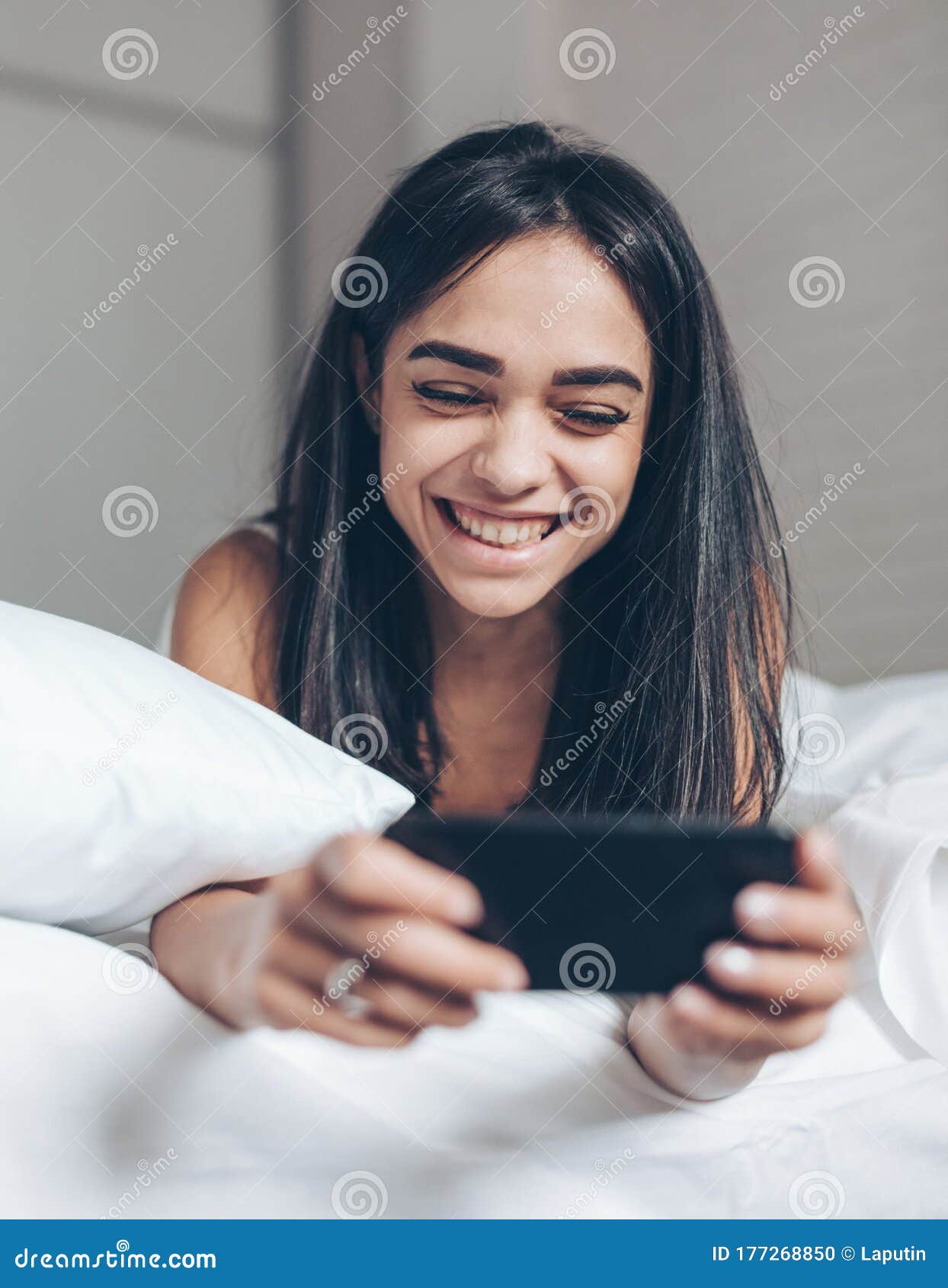 Happy Beautiful Woman Using Smartphone While Lying On Her Bed Smiling