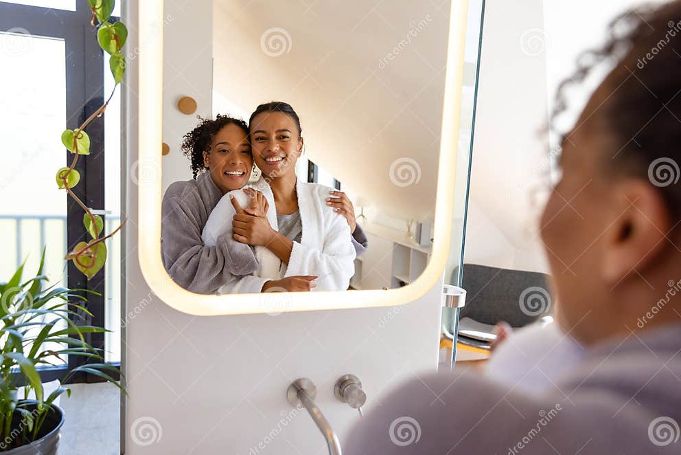 Happy Biracial Lesbian Couple In Bathrobes Hugging And Looking In