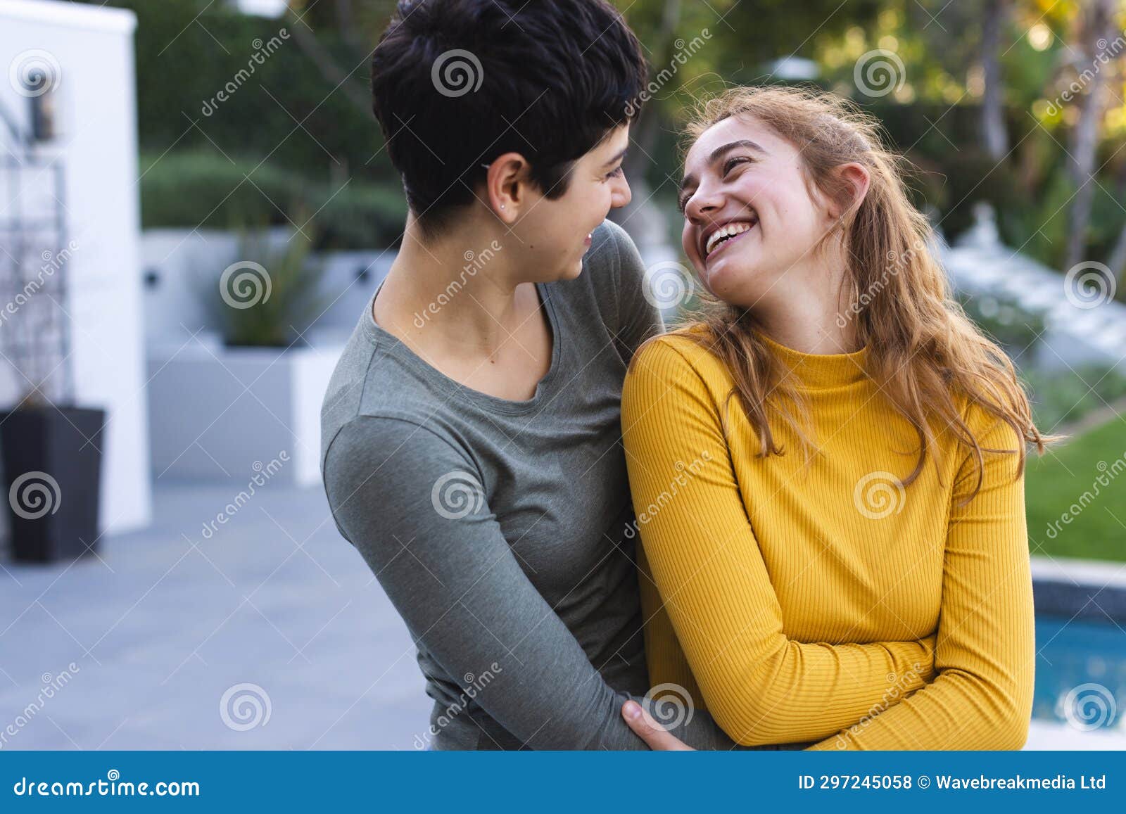 Happy Biracial Lesbian Couple On Garden Terrace Embracing And Smiling