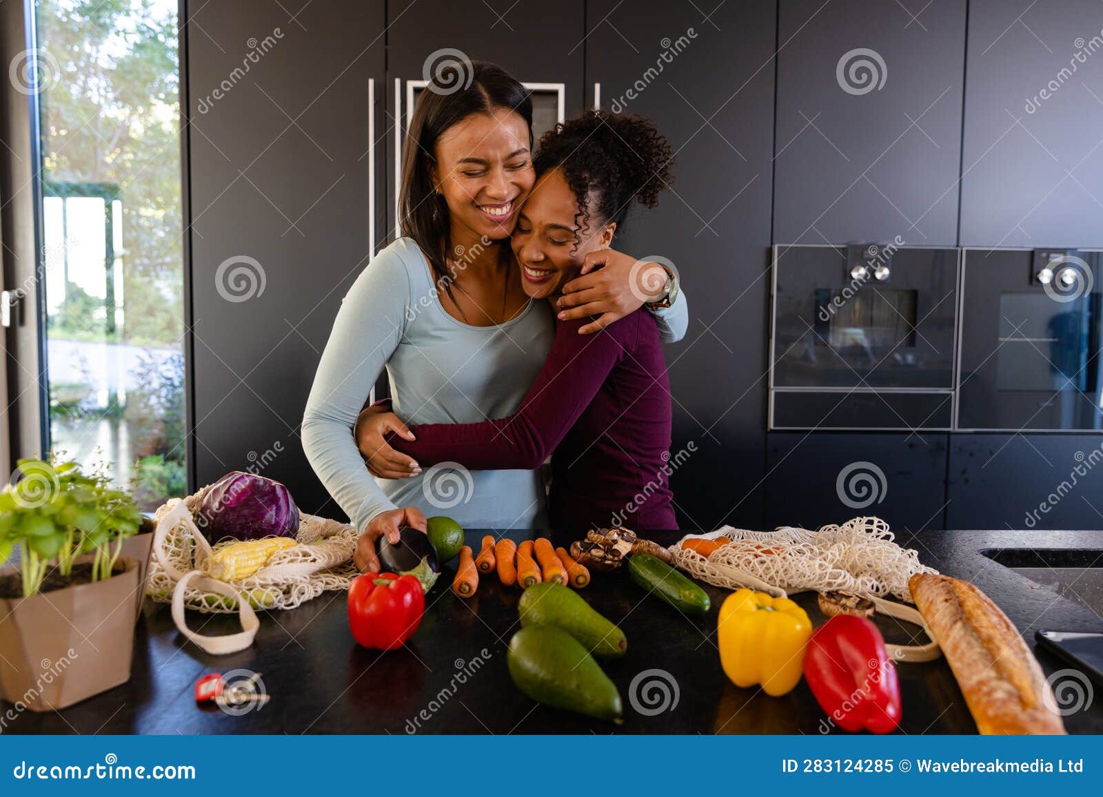 Happy Biracial Lesbian Couple Hugging And Unpacking Groceries In
