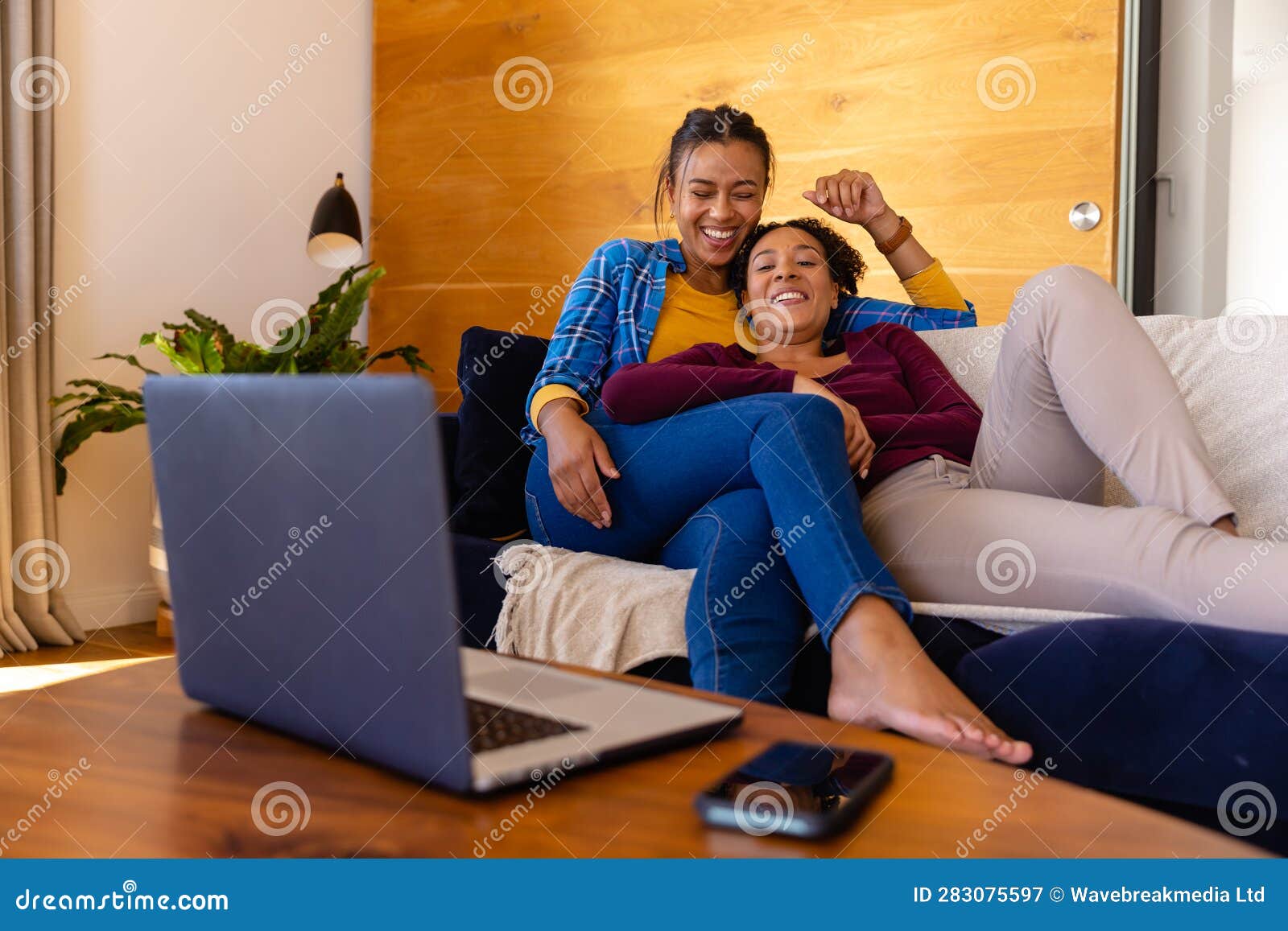 Happy Biracial Lesbian Couple Lying On Sofa And Using Laptop In Living