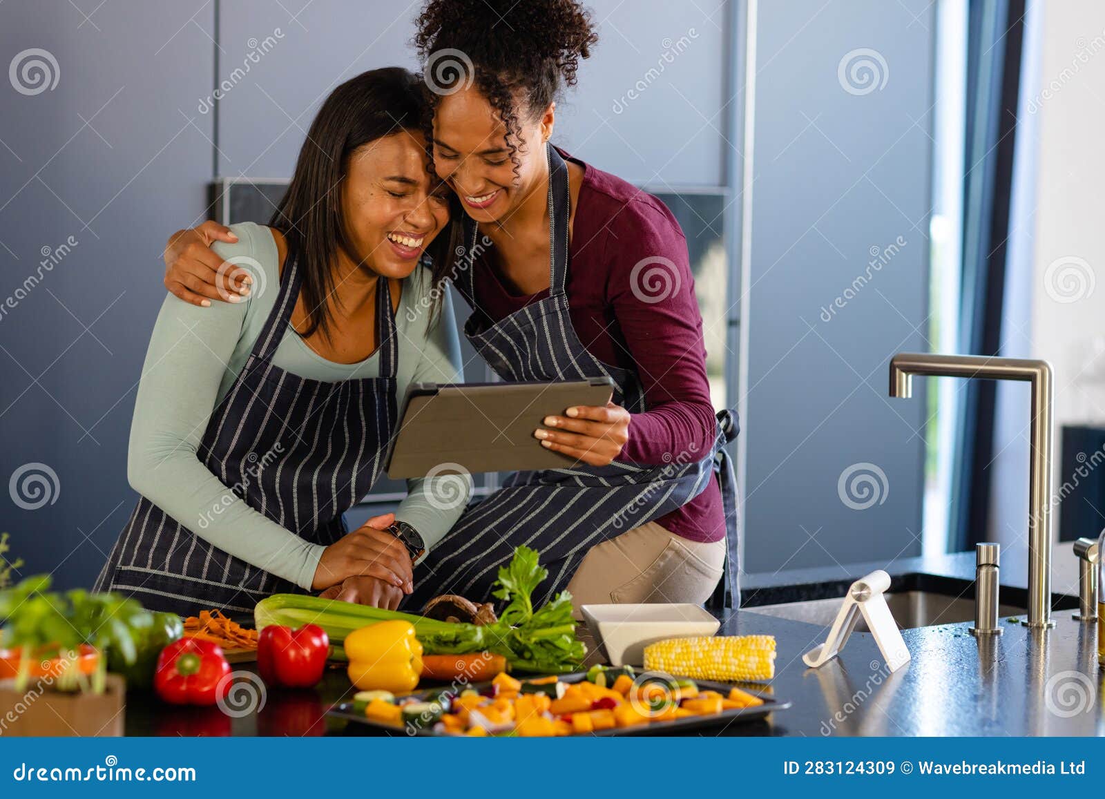 Happy Biracial Lesbian Couple Preparing Meal Using Tablet In Kitchen