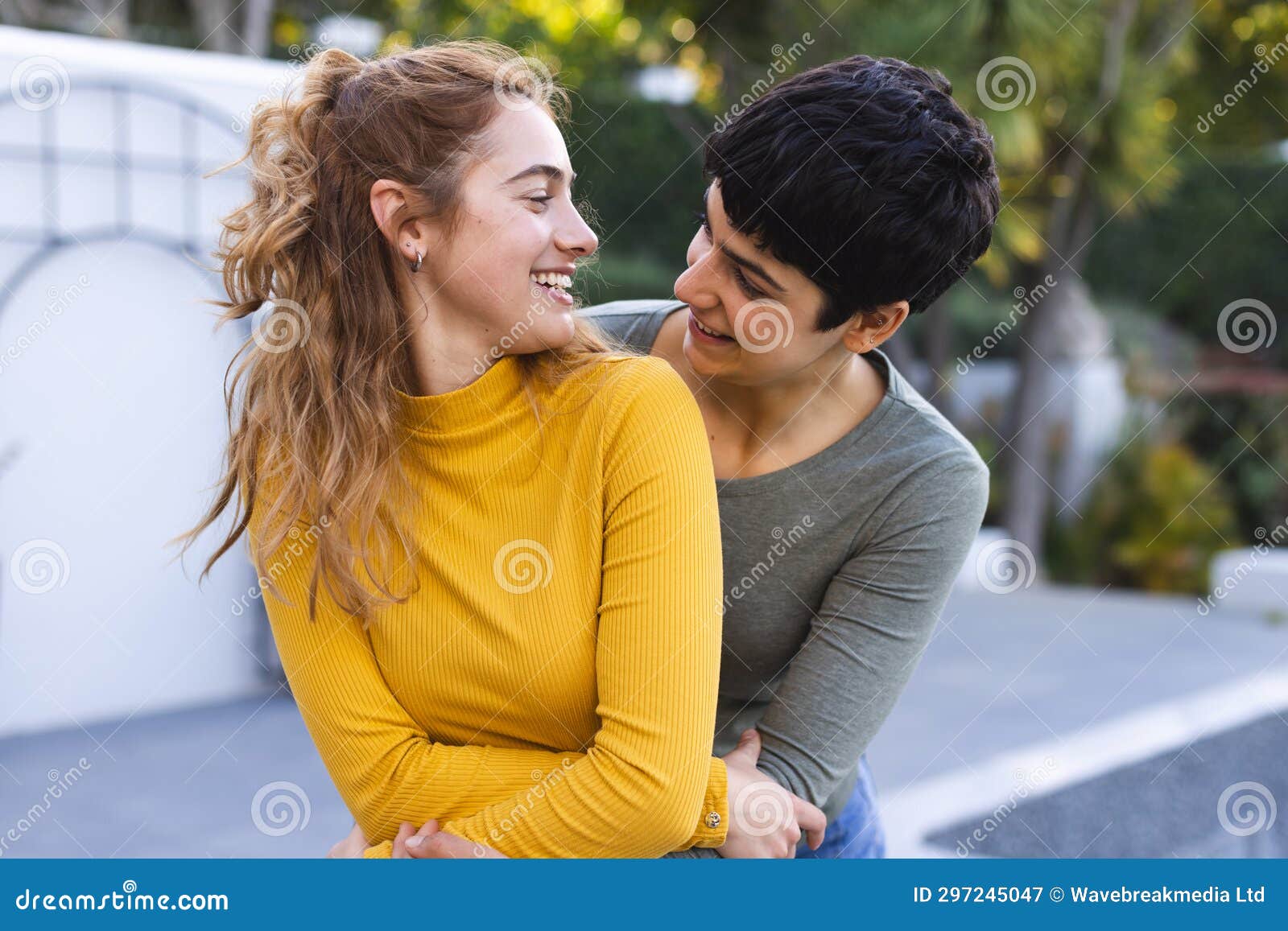 Happy Biracial Lesbian Couple Standing On Garden Terrace Embracing And