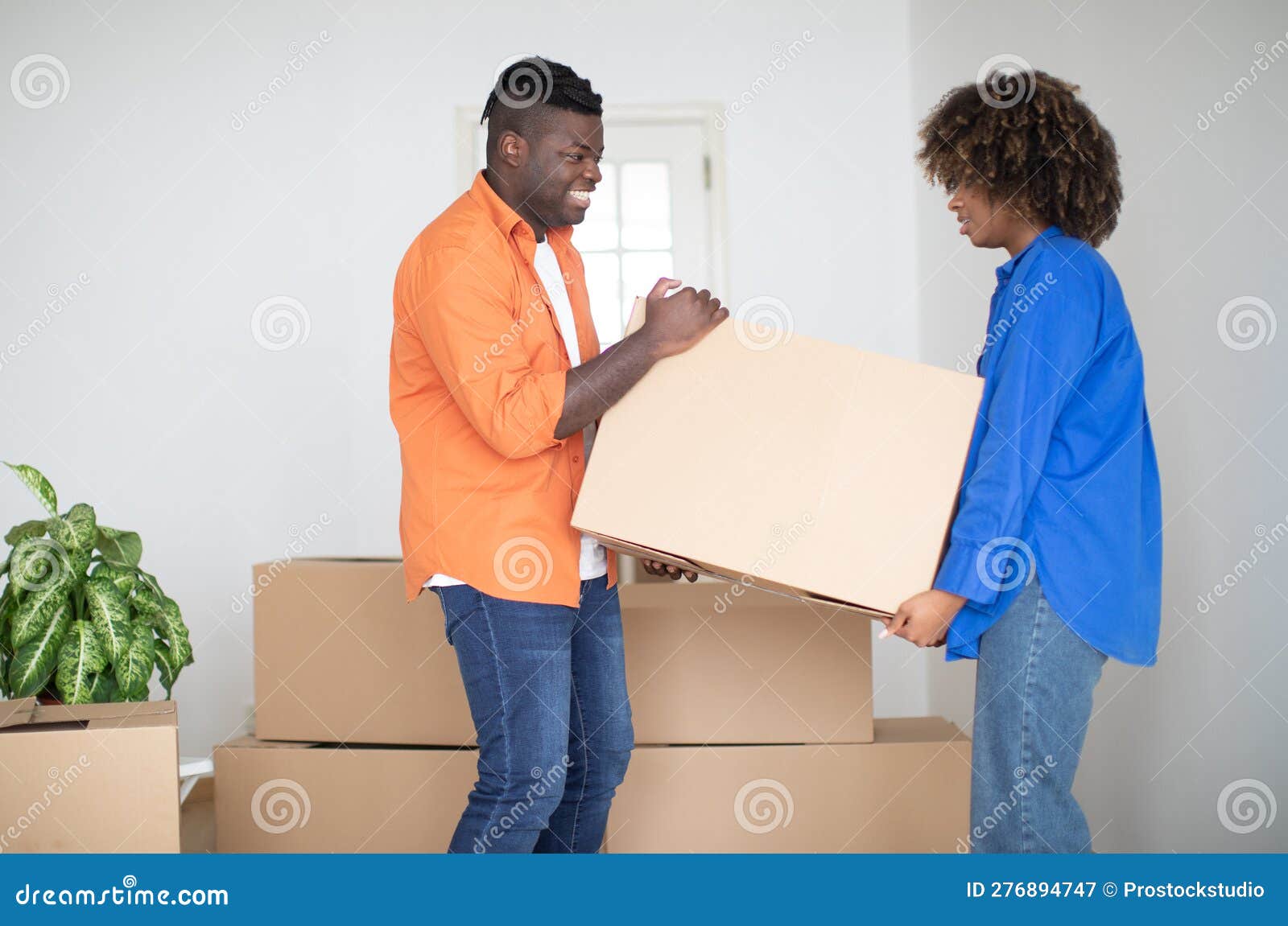 Happy Black Couple Carrying Big Cardboard Box Together On Moving Day