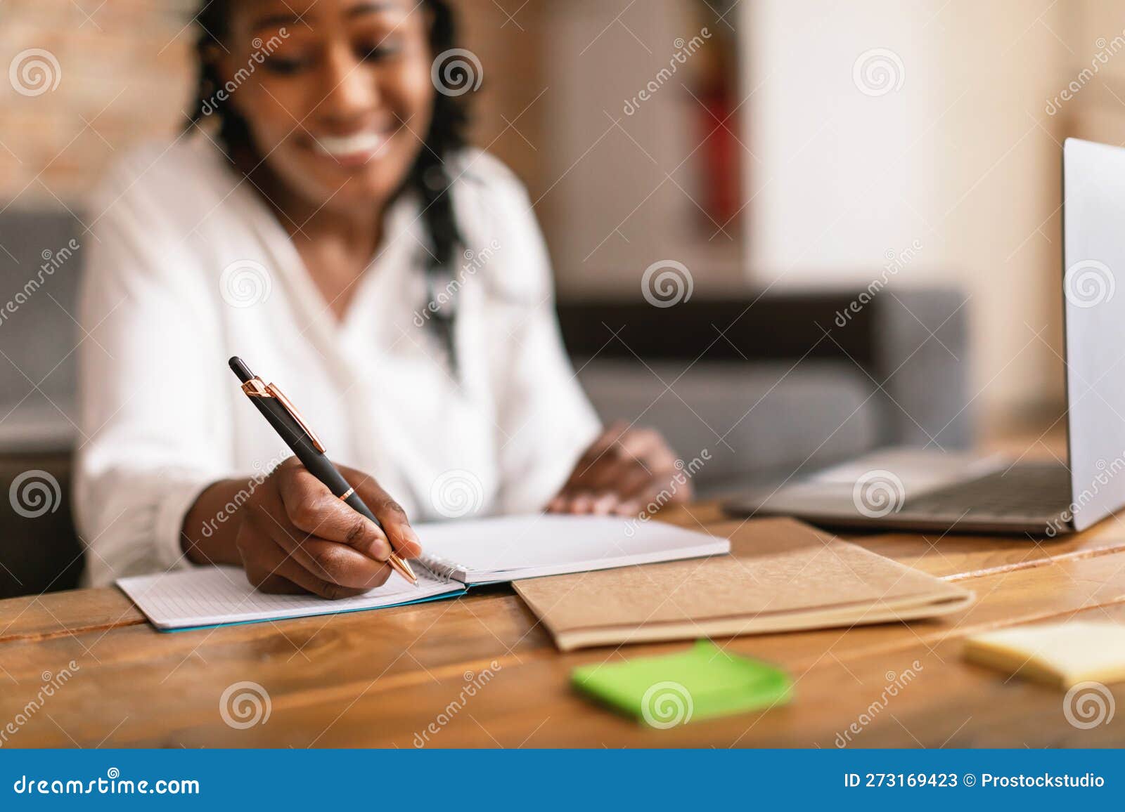 Happy Black Woman Writing in Notepad and Using Laptop, Noting ...