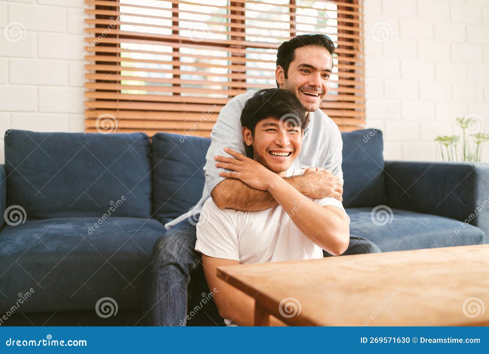 Happy Caucasian And Asian Lgbt Couple One Sitting On The Sofa