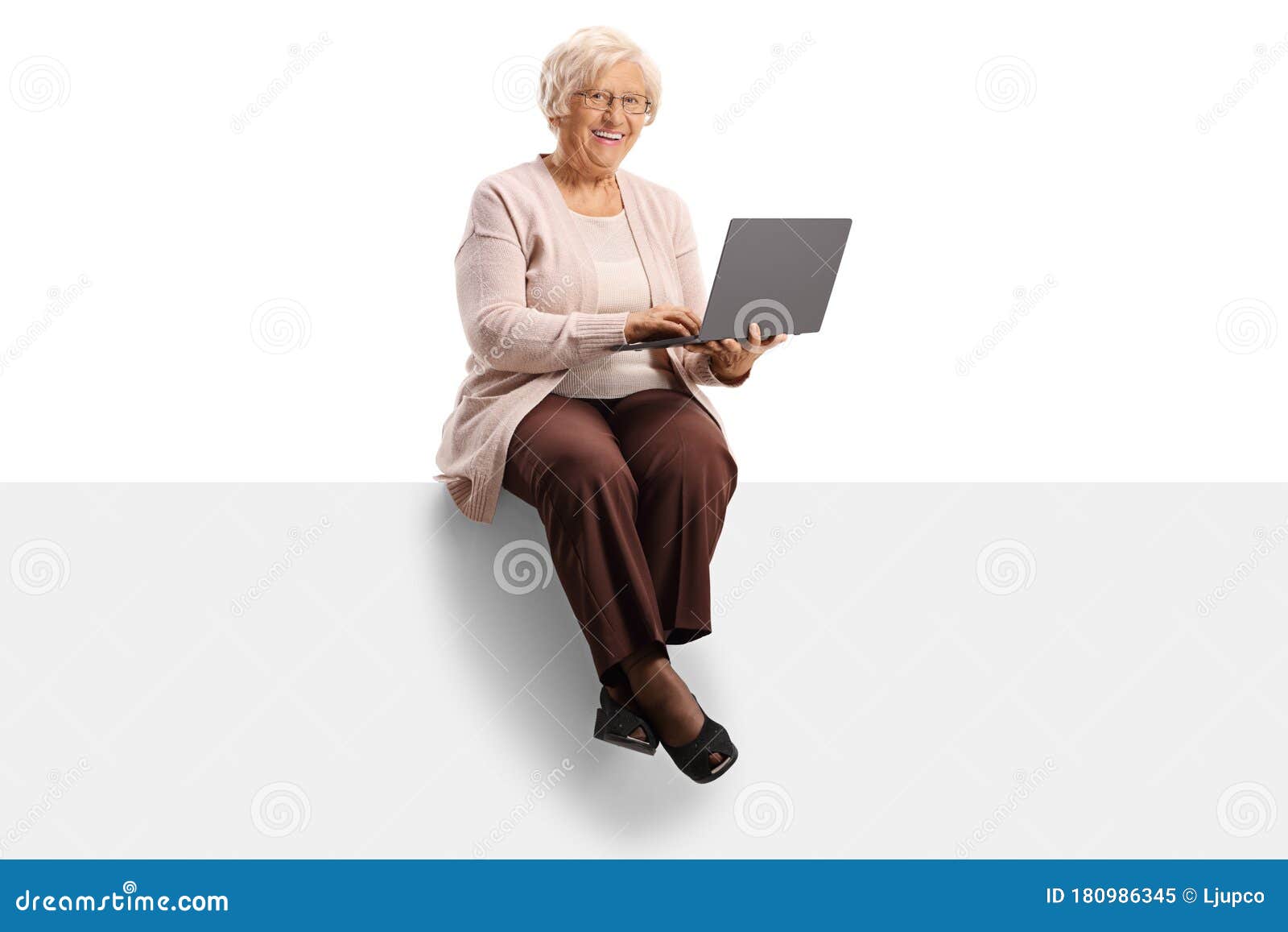 Happy Elderly Woman Sitting on a Blank Panel and Using a Laptop ...