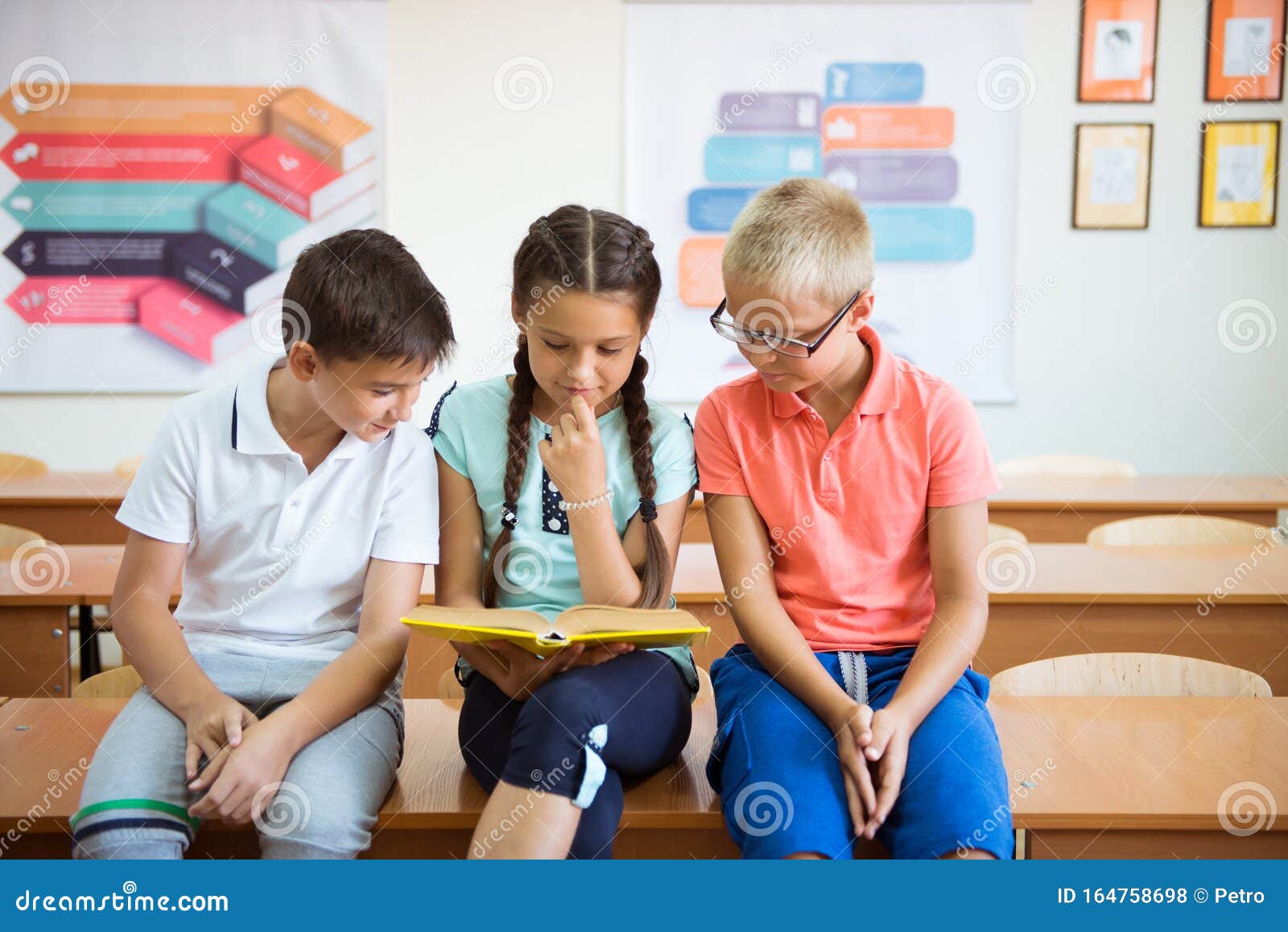 Happy Elementary Students Sitting on Desk with Book and Discussing in ...