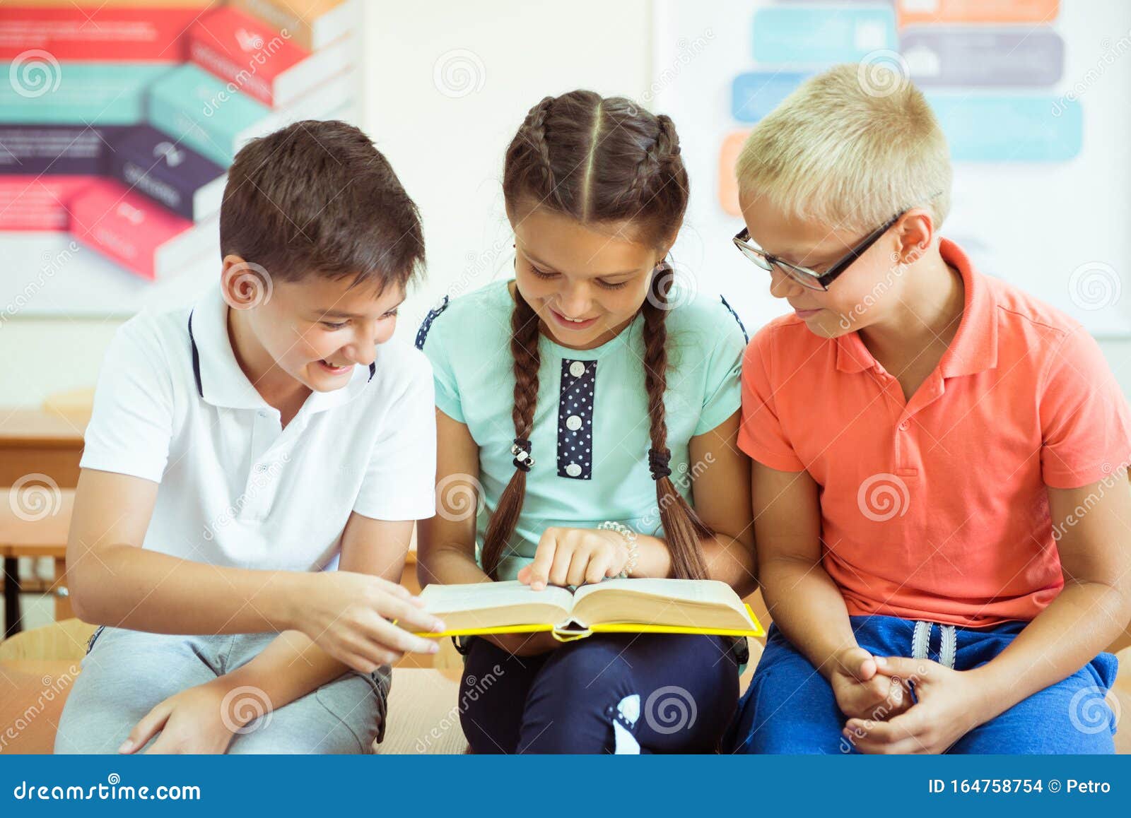 Happy Elementary Students Sitting on Desk with Book and Discussing in ...