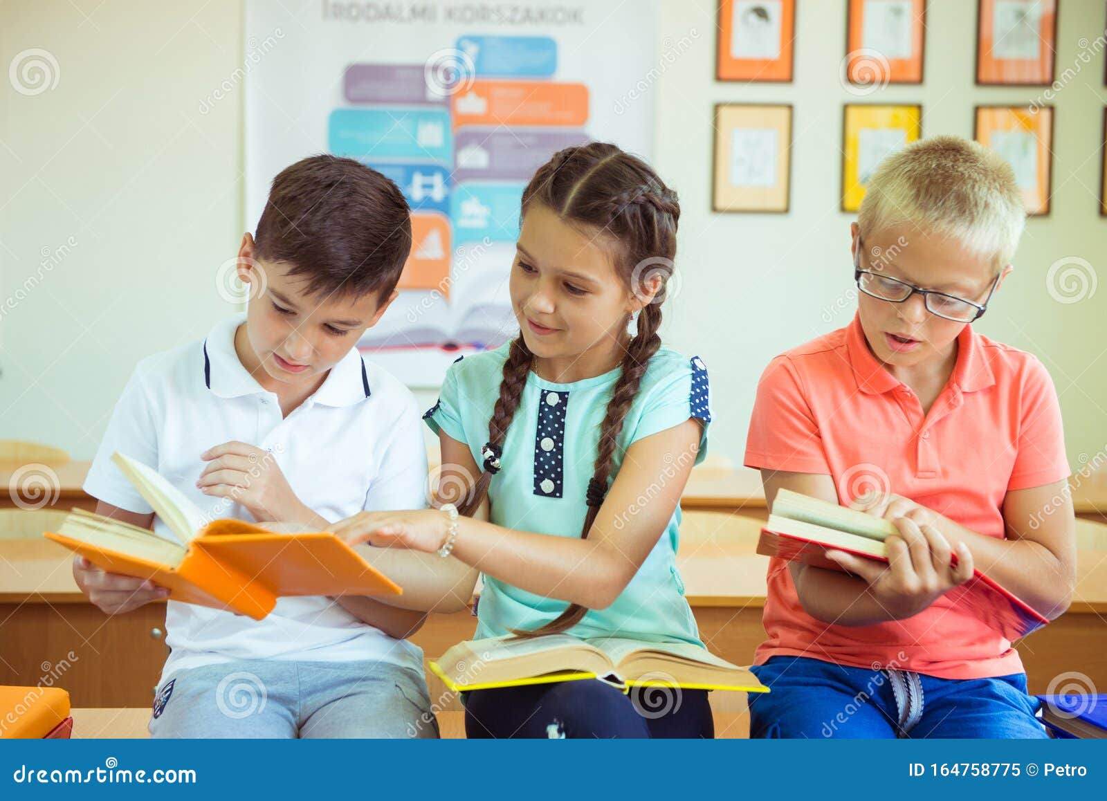 Happy Elementary Students Sitting on Desk with Book and Discussing in ...