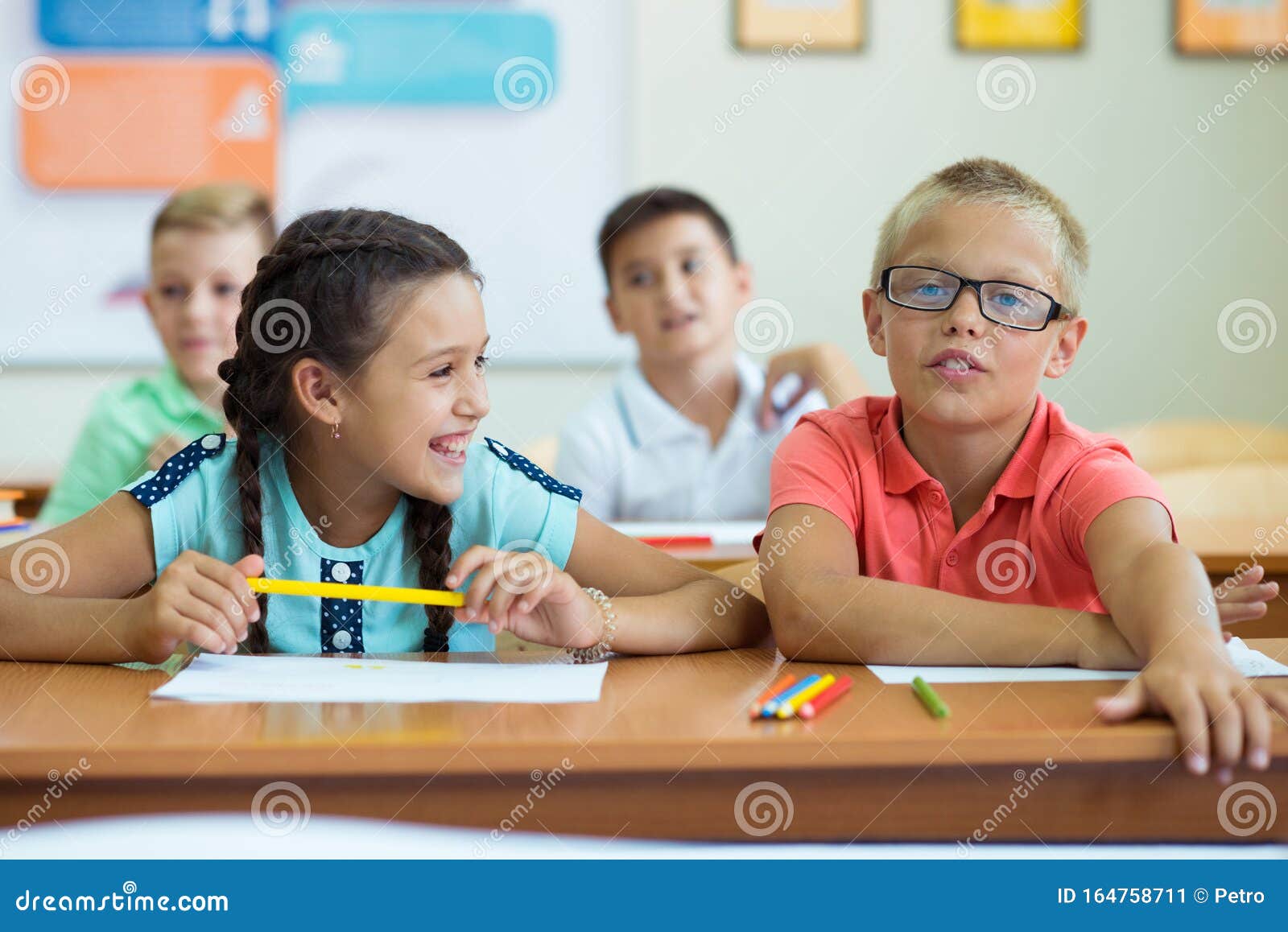 Happy Elementary Students Sitting at Desk and Joyful Discussing in ... Happy Elementary Students Sitting at Desk and Joyful Discussing in ...