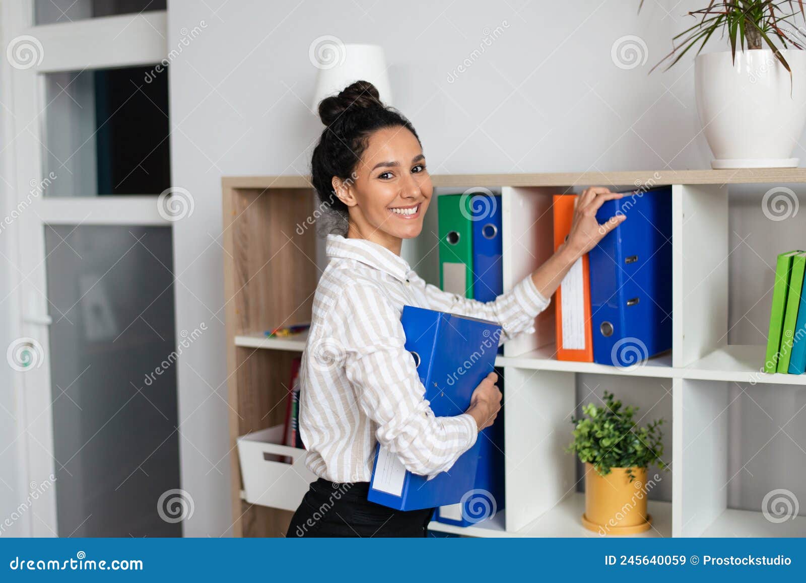 Happy Female Office Worker Taking Folders from Shelf, Looking and ...