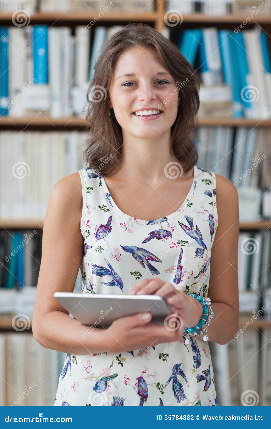 Happy Female Student Against Bookshelf Holding Tablet PC in Library ...