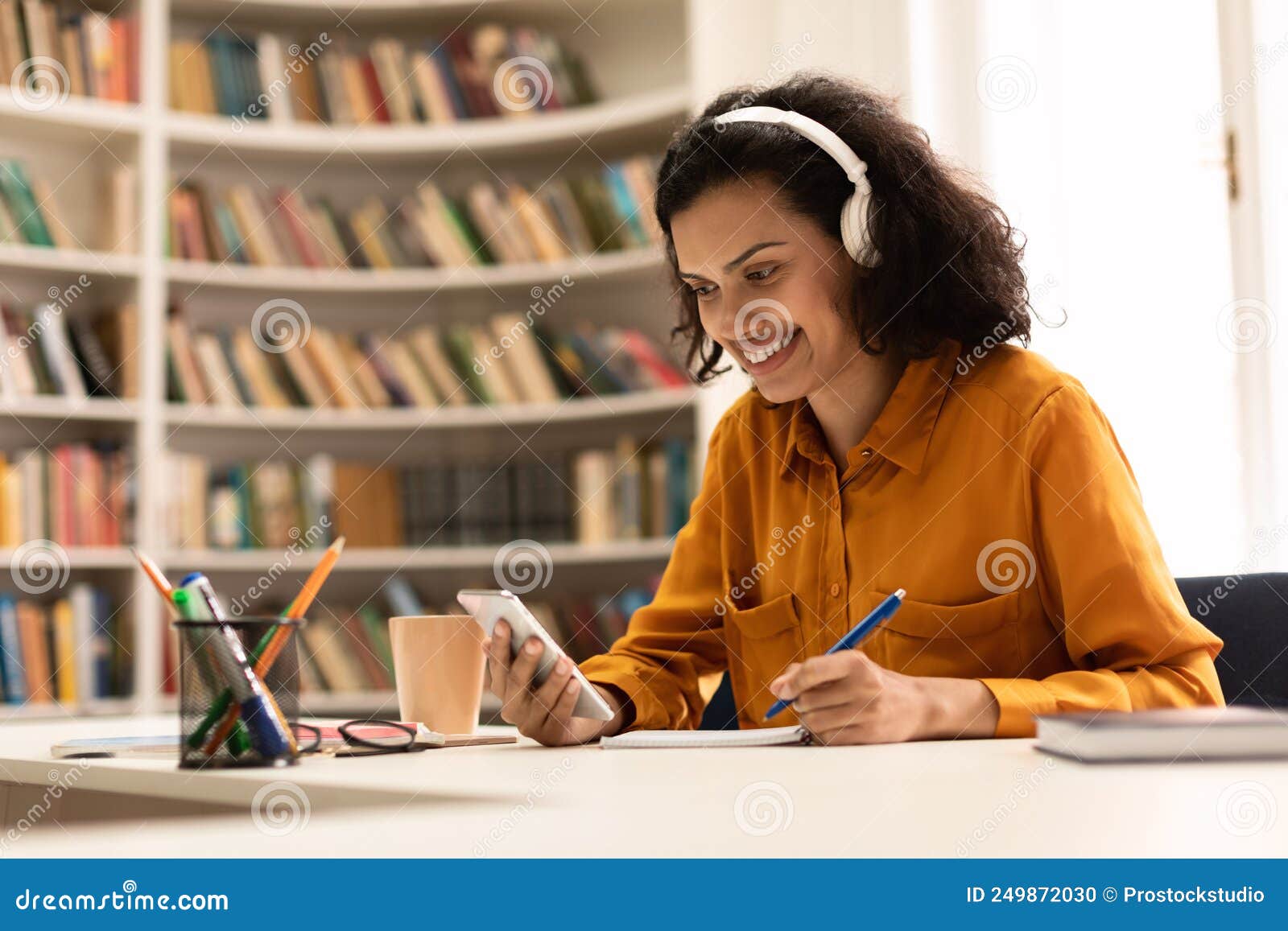 Happy Female Student Sitting in Library, Using Cellphone and Taking ...