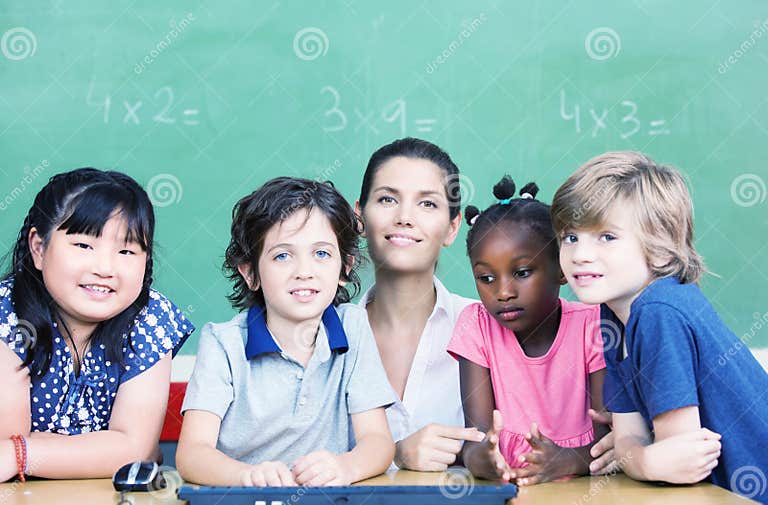 Happy Female Teacher With Her Multirace Classroom At School Desk Stock