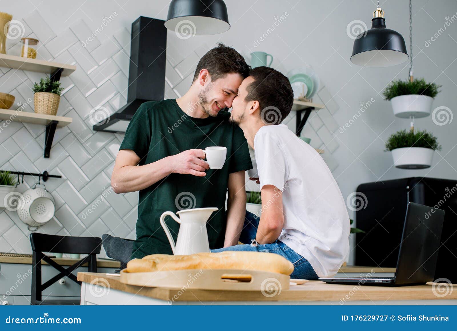 Happy Gay Couple Having Breakfast In Kitchen And Using Laptop Amorous Gay Men Kissing Each