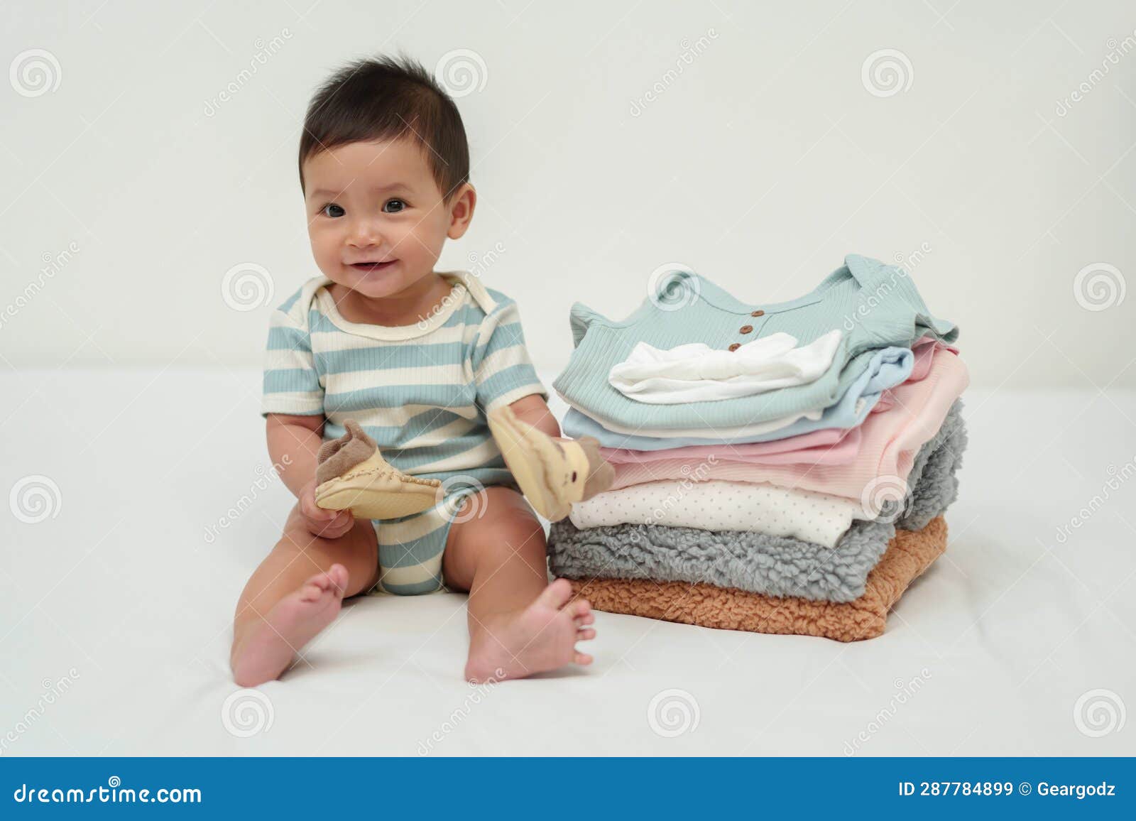 Happy Infant Sitting with Stack of Baby Clothes on Bed Stock Image ...