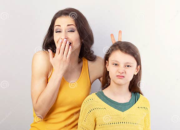 Happy Laughing Mother Showing The Horns Above Her Daughter Head And