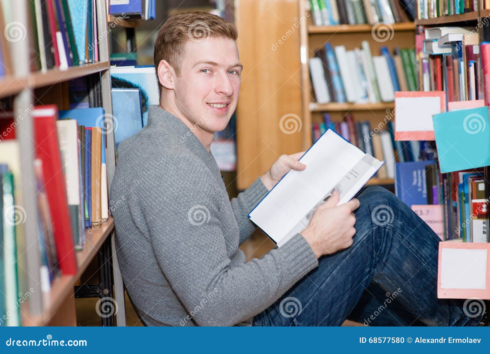 Happy Male Student with Book Sitting on Floor in Library Stock Photo ...