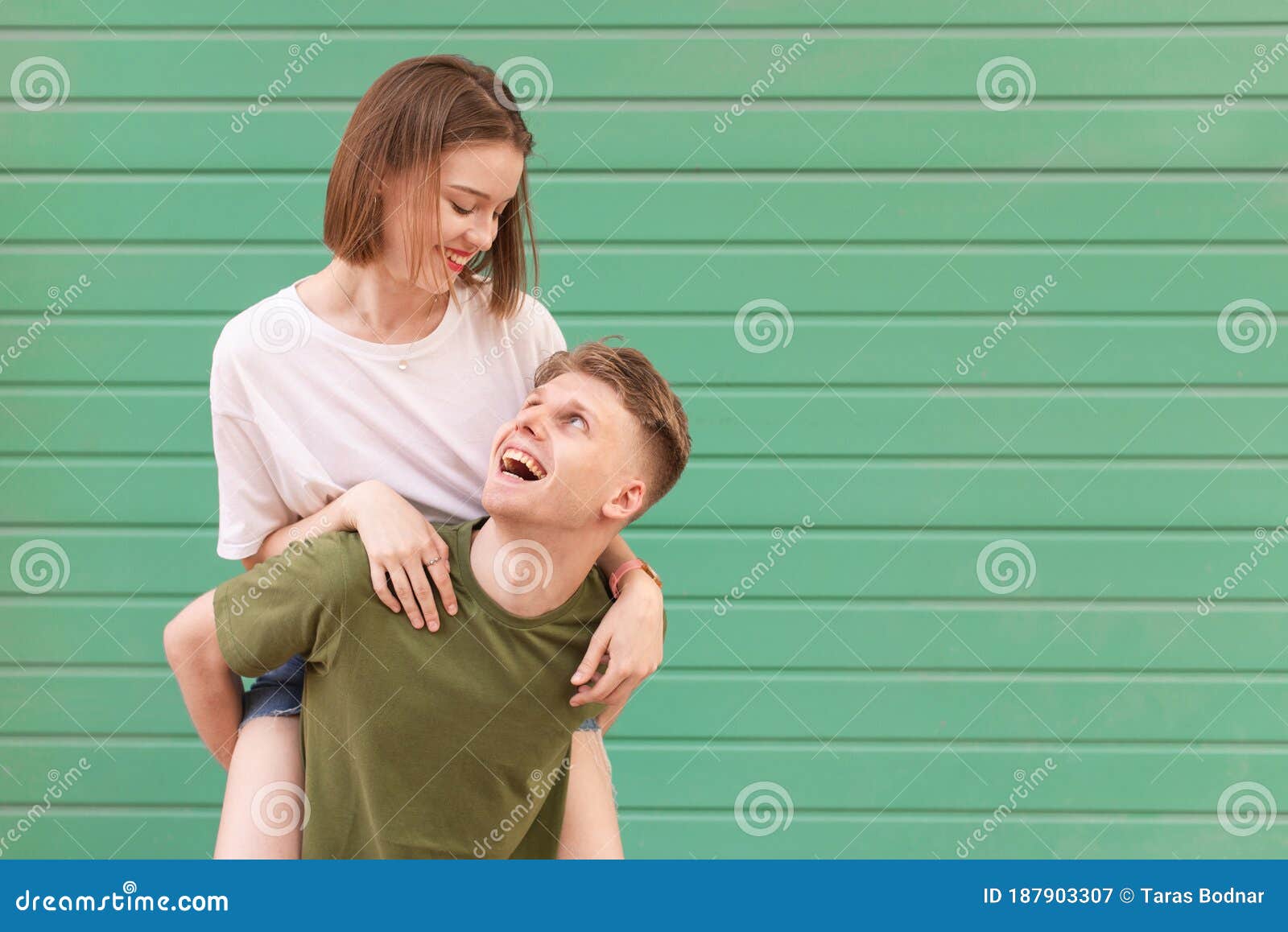Happy Man Carries His Girlfriend On His Back Looking At Her And