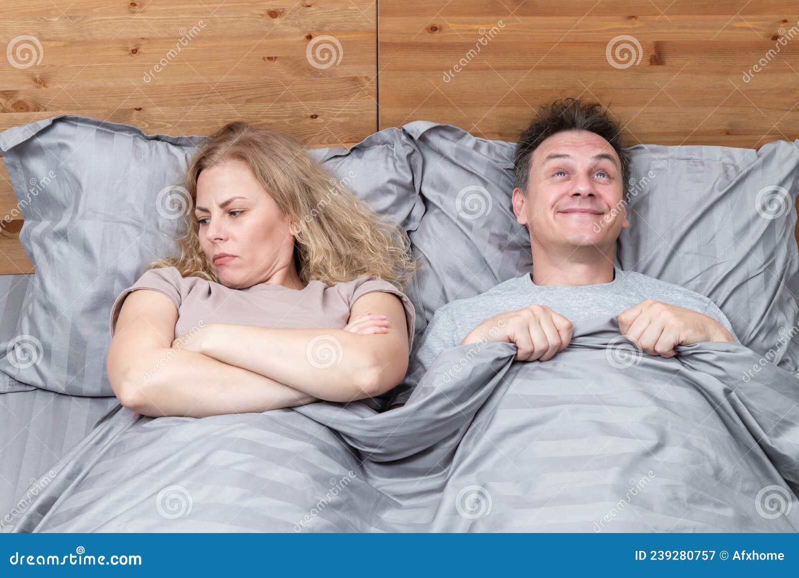 Happy Man And Disgruntled Woman Lying In Bed Under The Covers