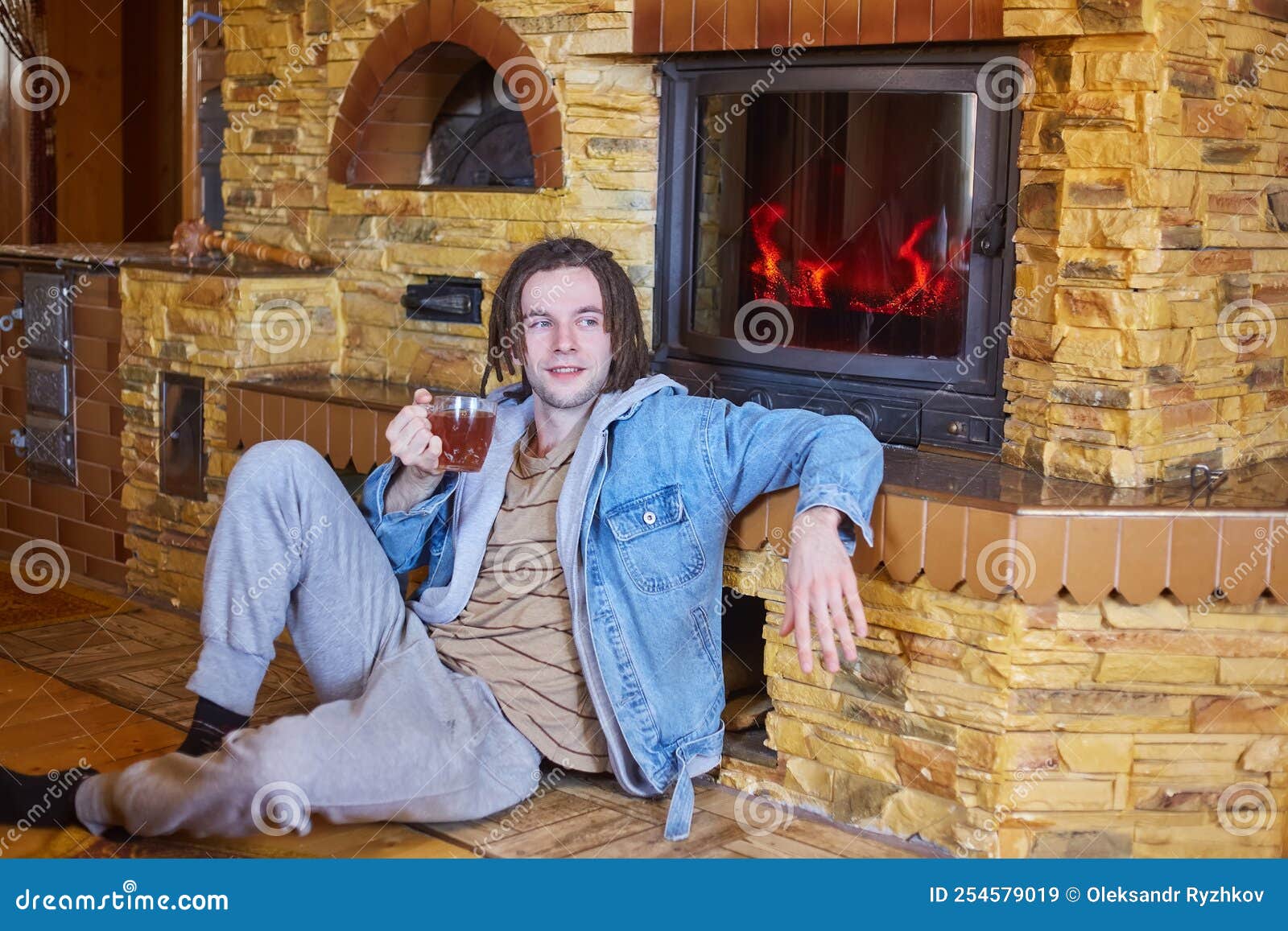 Happy Man Sits in Front of a Fireplace and Holds a Cup. Smiling Guy in ...
