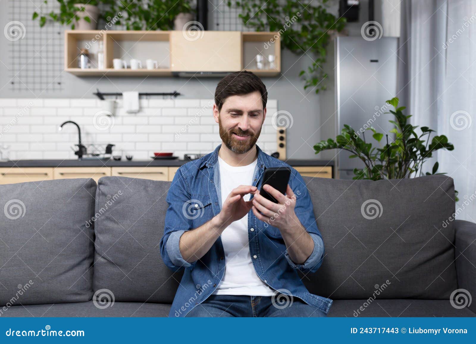 Happy Man Smiling and Using Phone Sitting on Sofa at Home Stock Image ...