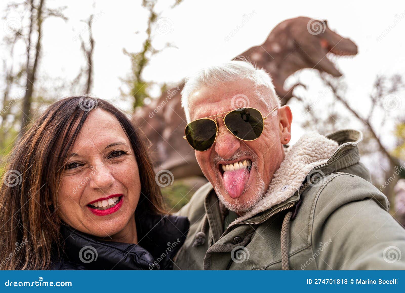 Happy Middle Aged Couple Taking A Selfie In Front A Model T Rex In A
