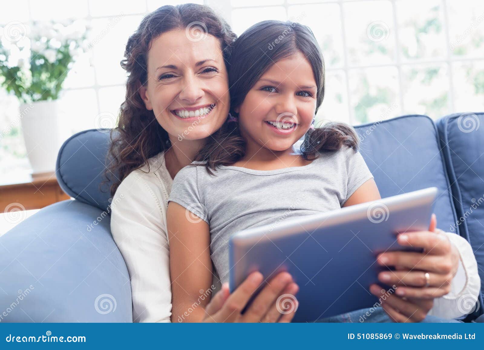 Happy Mother And Daughter Sitting On The Couch And Using Tablet Stock
